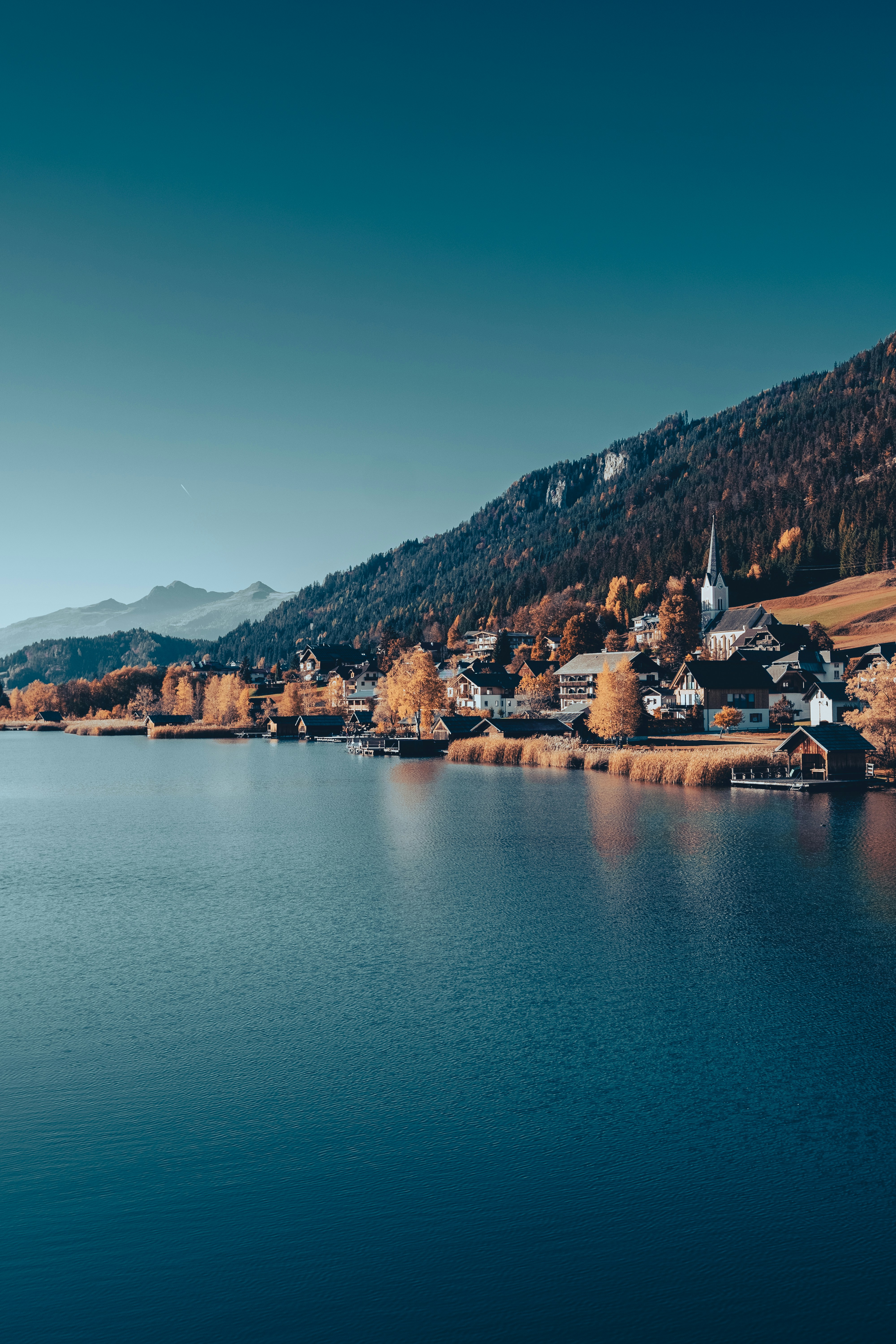 Charming lakeside village nestled against a backdrop of majestic mountains, showcasing autumn foliage and serene waters.