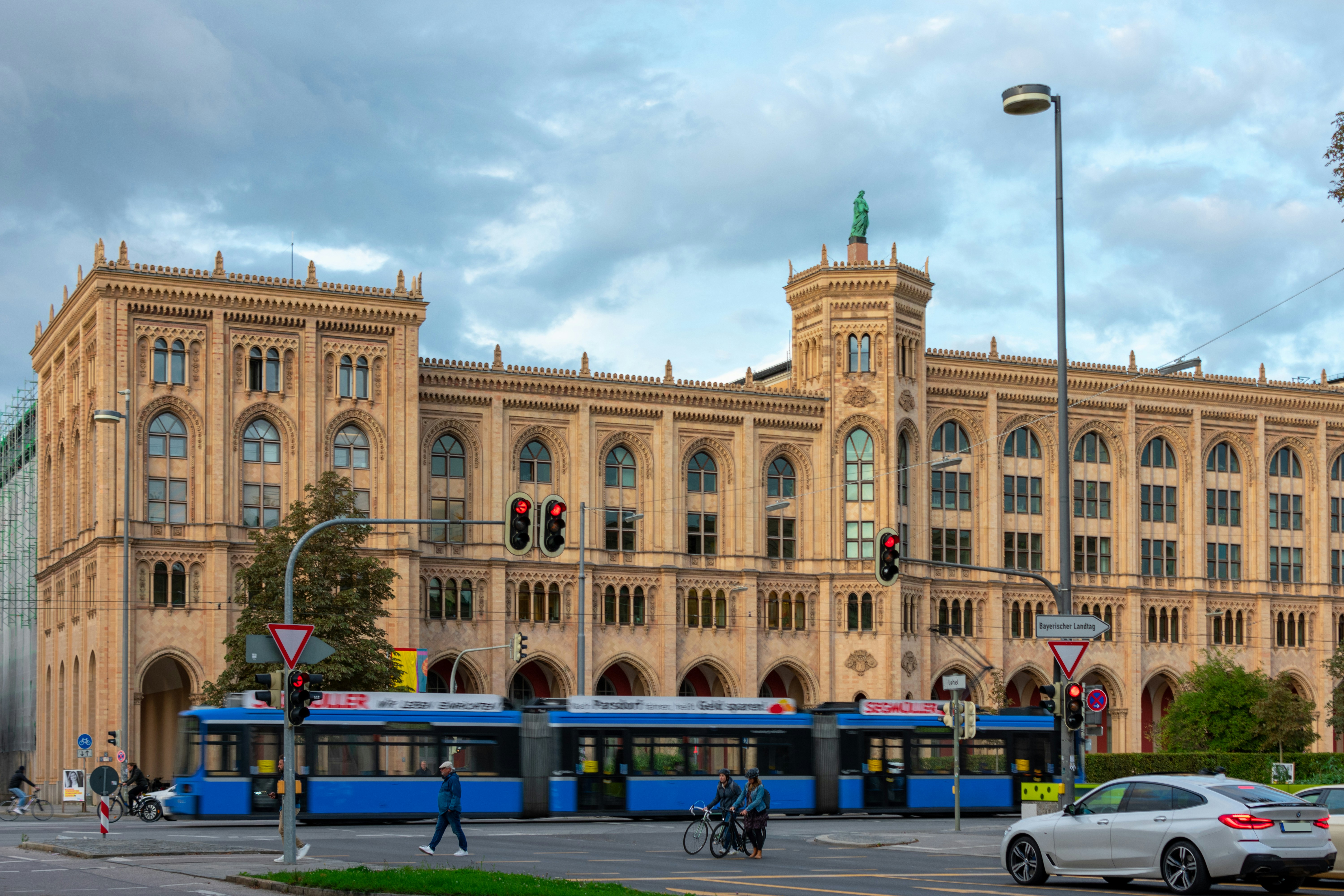 Historical building with intricate architecture alongside a busy street, featuring a tram and traffic lights.