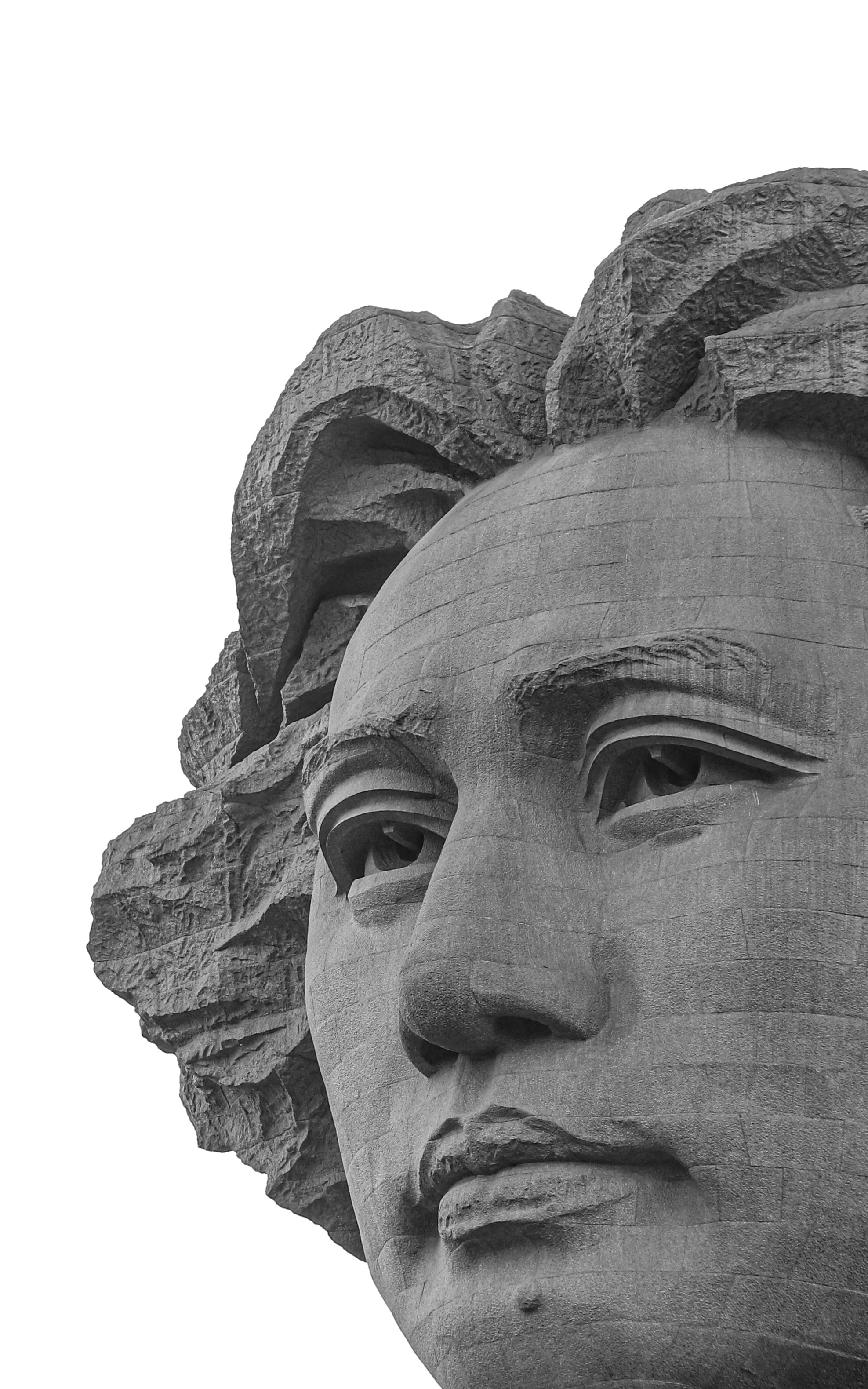 Close-up of a monumental sculpture's face, showcasing intricate details and textures in monochrome. The expression conveys a sense of contemplation.