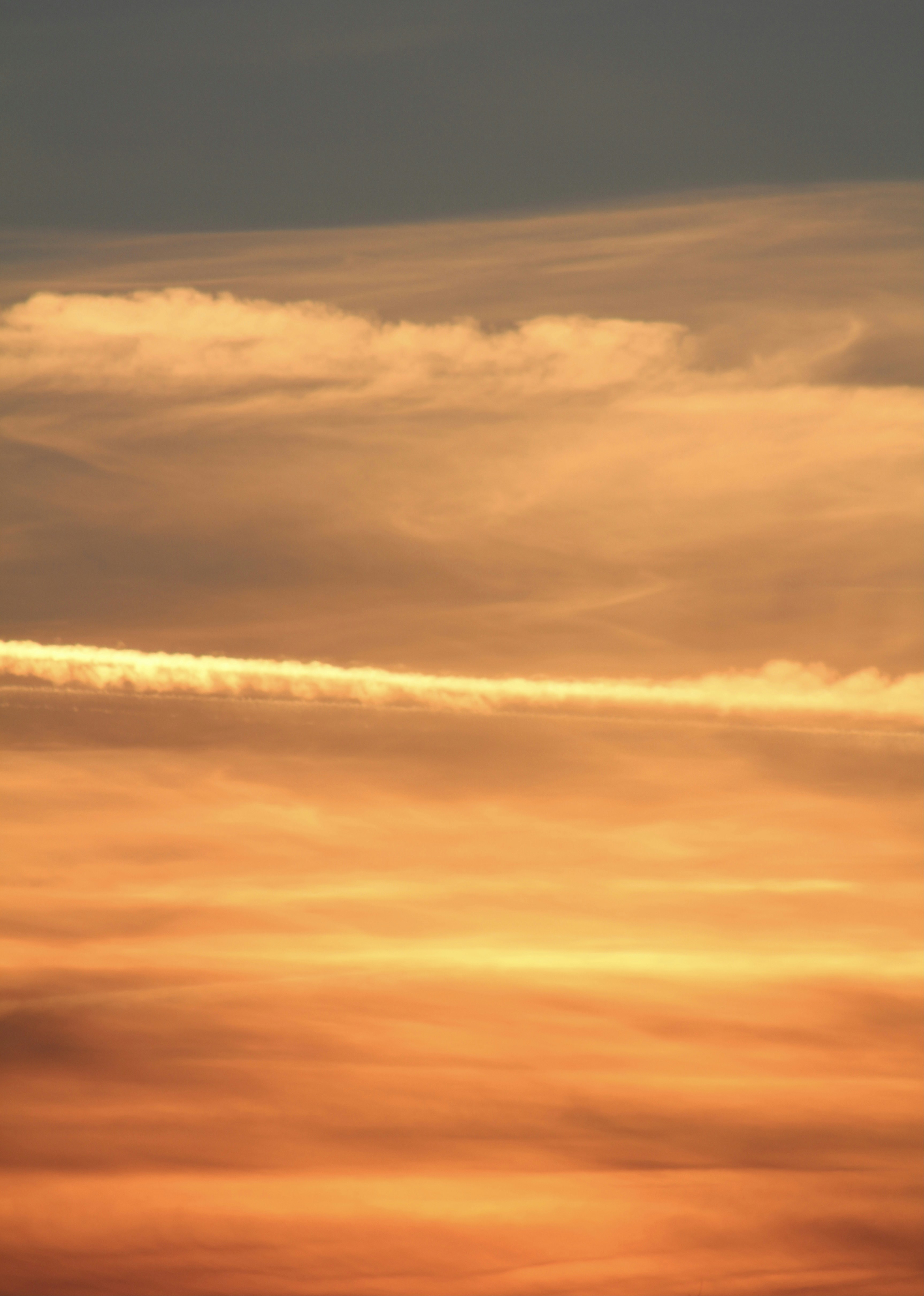 Soft hues of orange and gold blend seamlessly in a tranquil sunset sky, with wispy clouds tracing delicate patterns.
