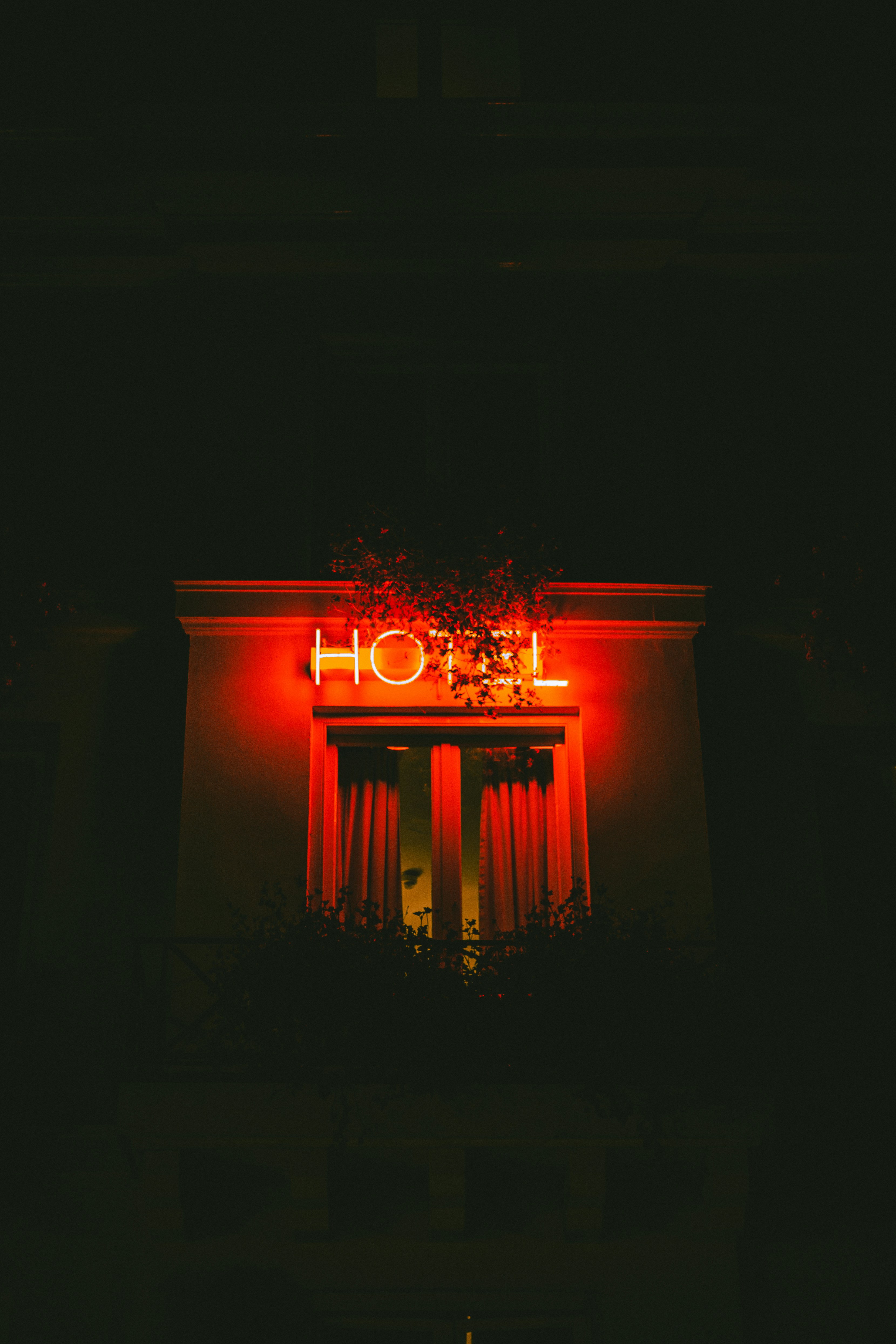 Illuminated hotel sign glowing in red against a dark backdrop, framed by curtains and foliage.