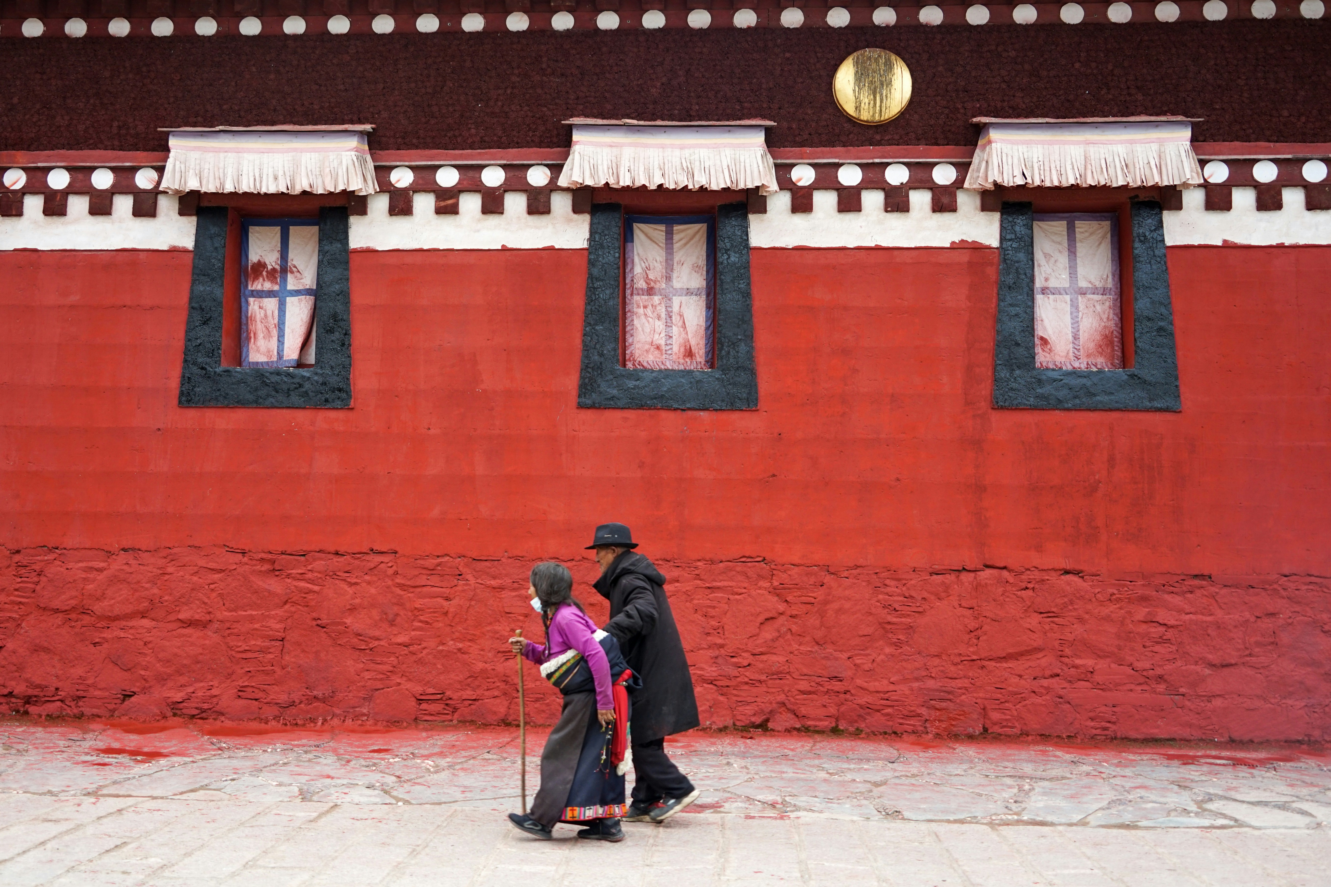 Scarlet Wall Stroll: Quiet Figures Against a Monastic Facade