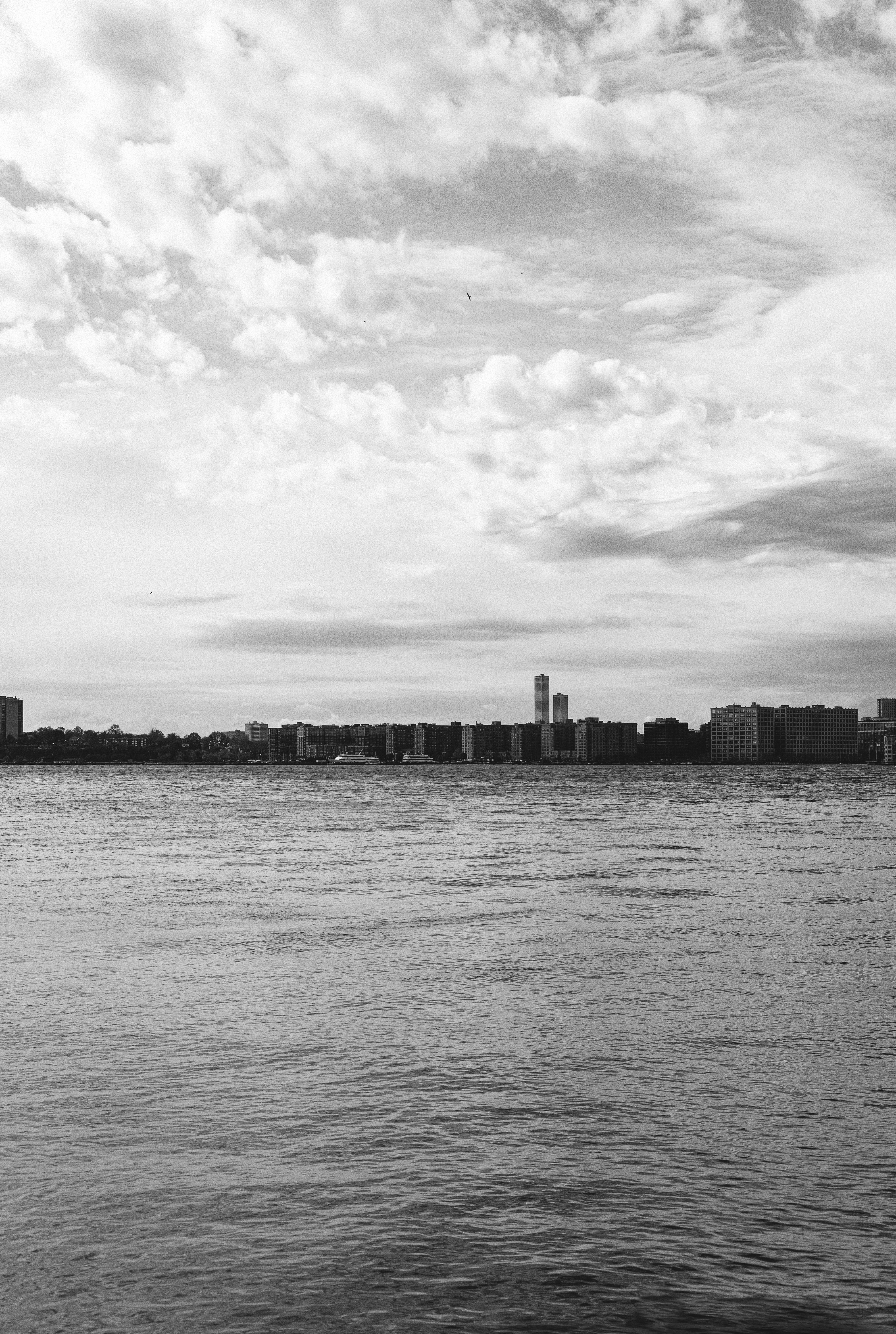 Dramatic black and white view of a city skyline reflecting on calm waters under a cloudy sky.