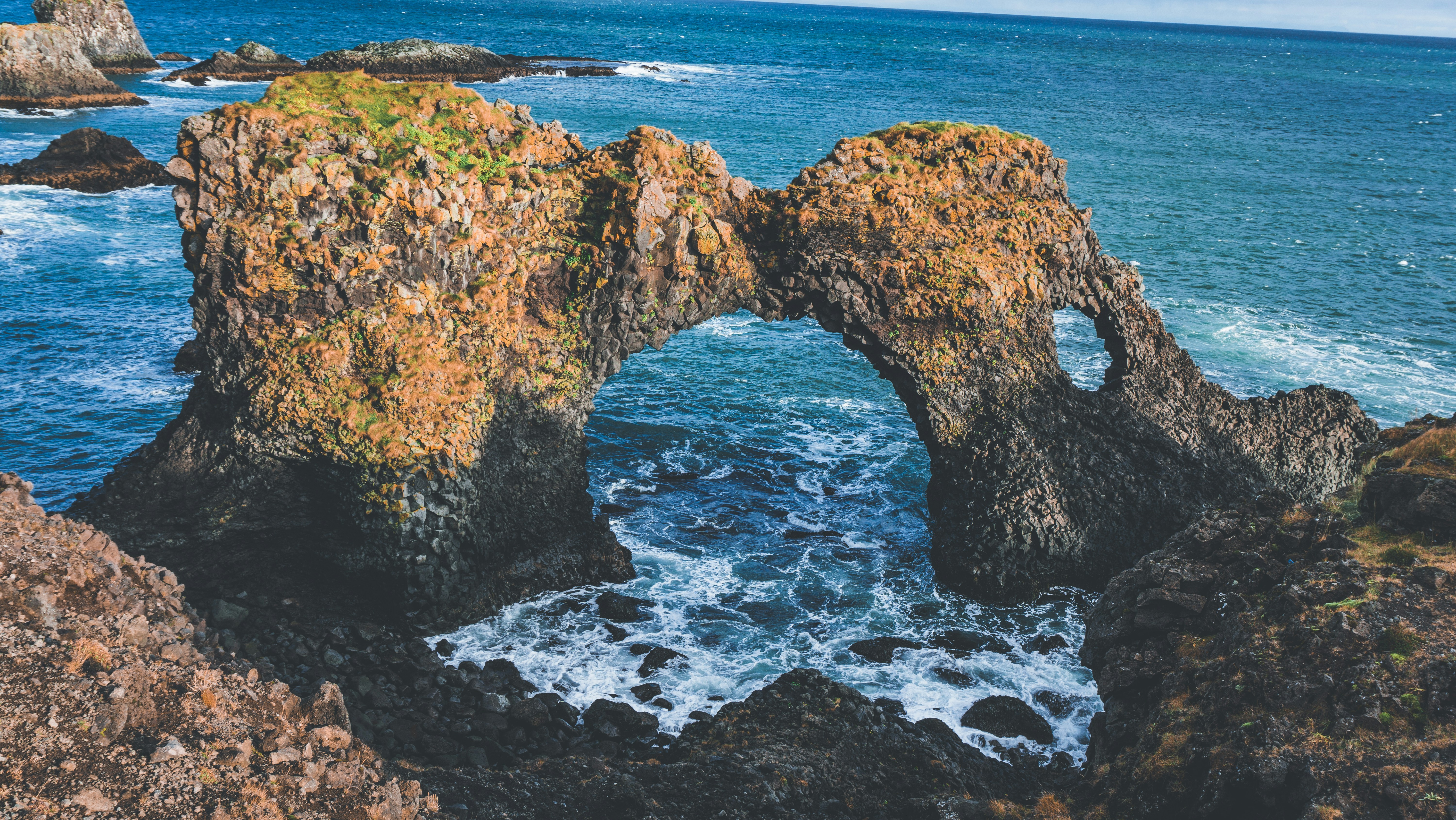 Natural rock arch formation surrounded by crashing waves and rugged coastline, showcasing the beauty of coastal geology.