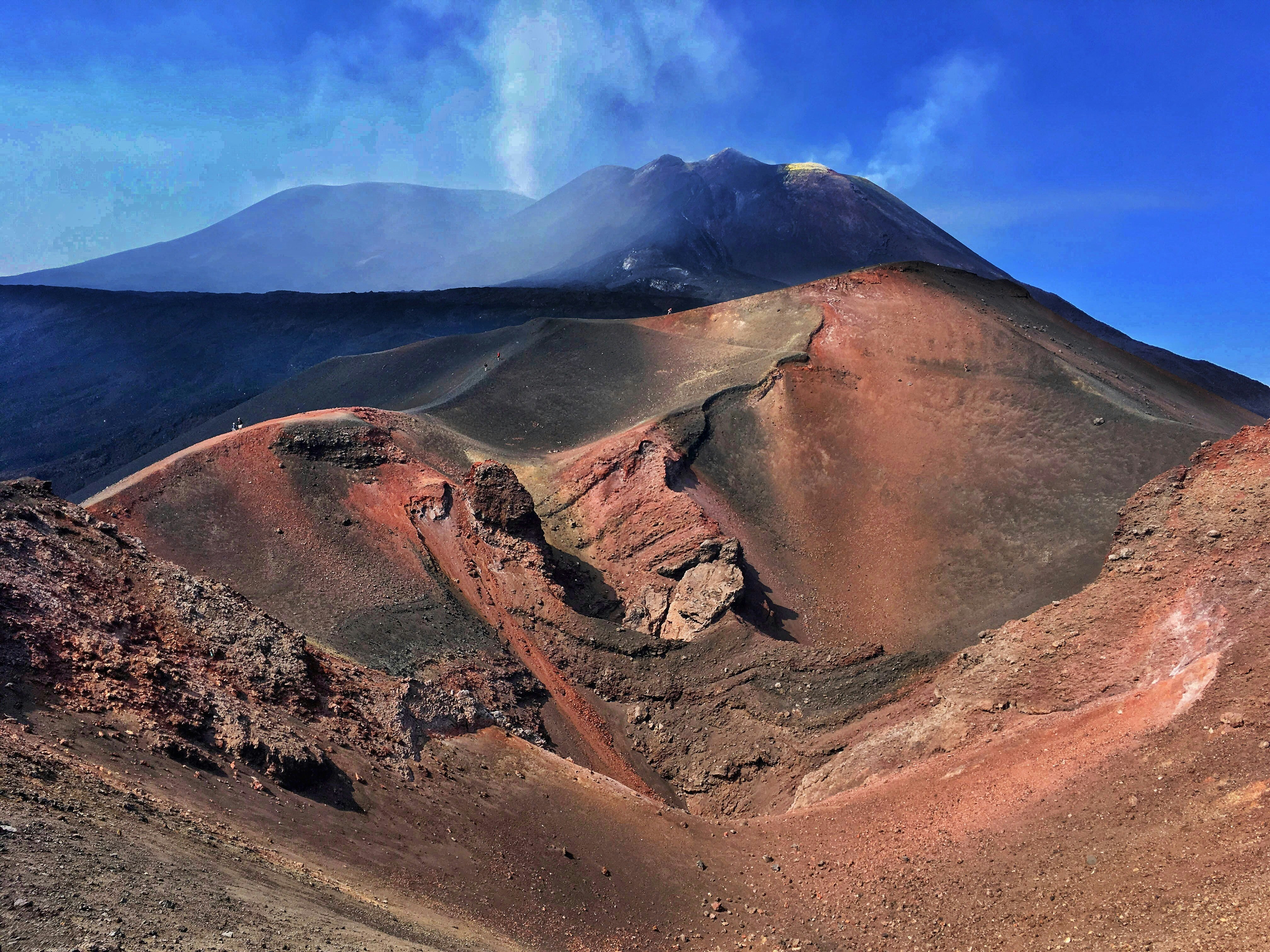 Rugged volcanic slopes of Mount Etna with smoke rising against a clear blue sky.