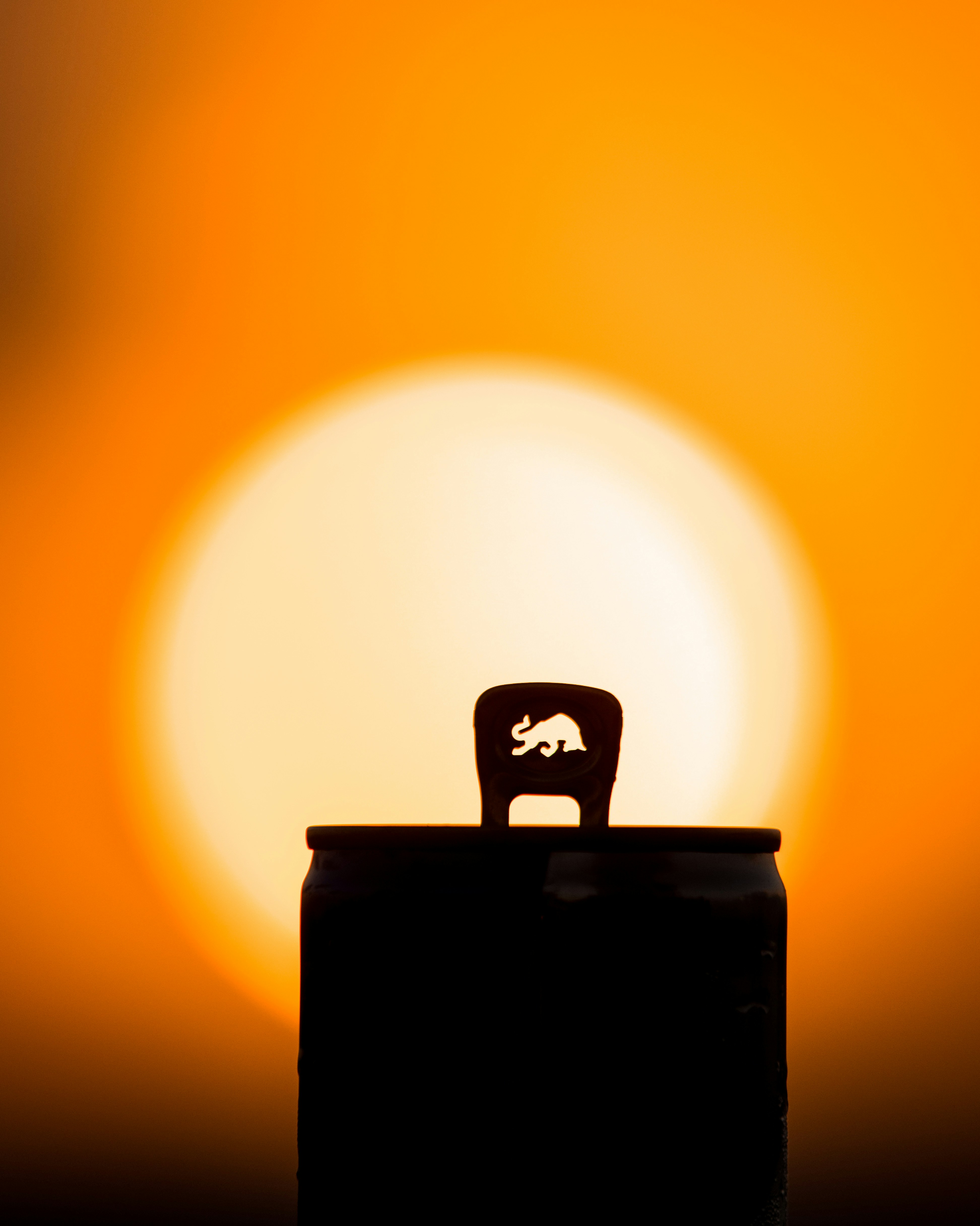 Bronze Dawn: Silhouette of a Can Tab Framed by a Fiery Sun