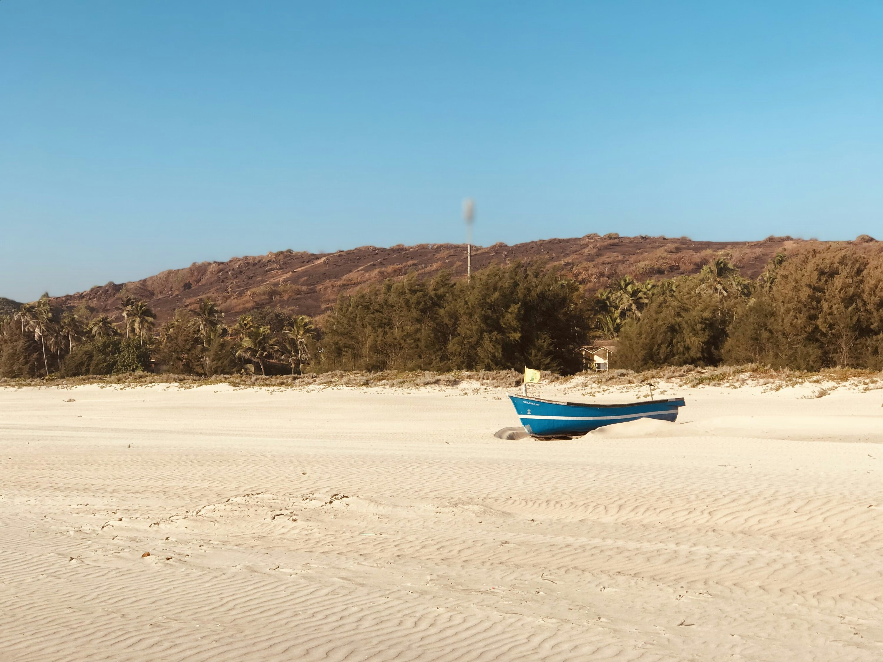 Blue Rowboat Resting on Sun-Soaked Beach Beneath a Clear Coastal Sky
