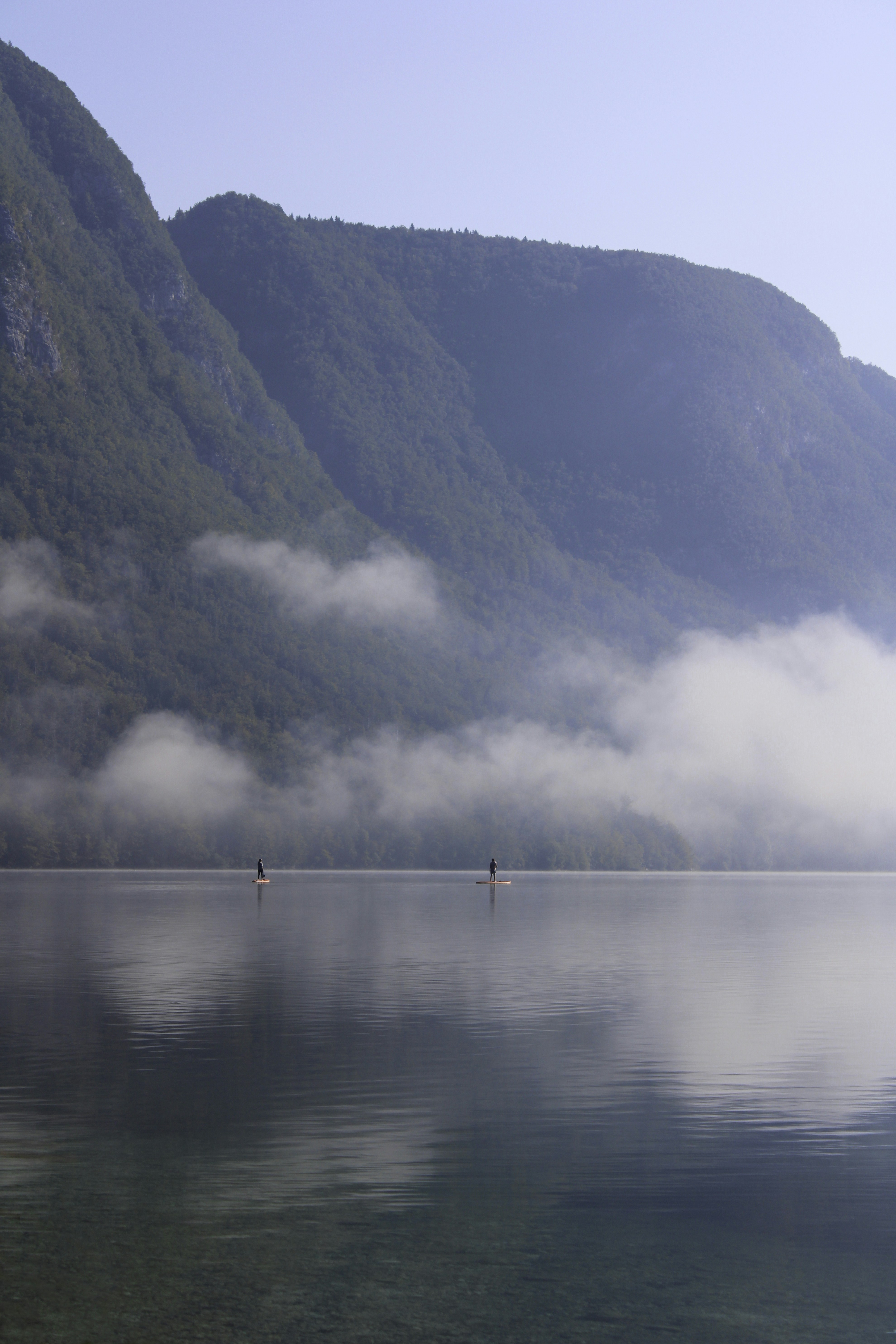 Glassy Alpine Lake: Two Paddleboarders Amid Mountain Mist