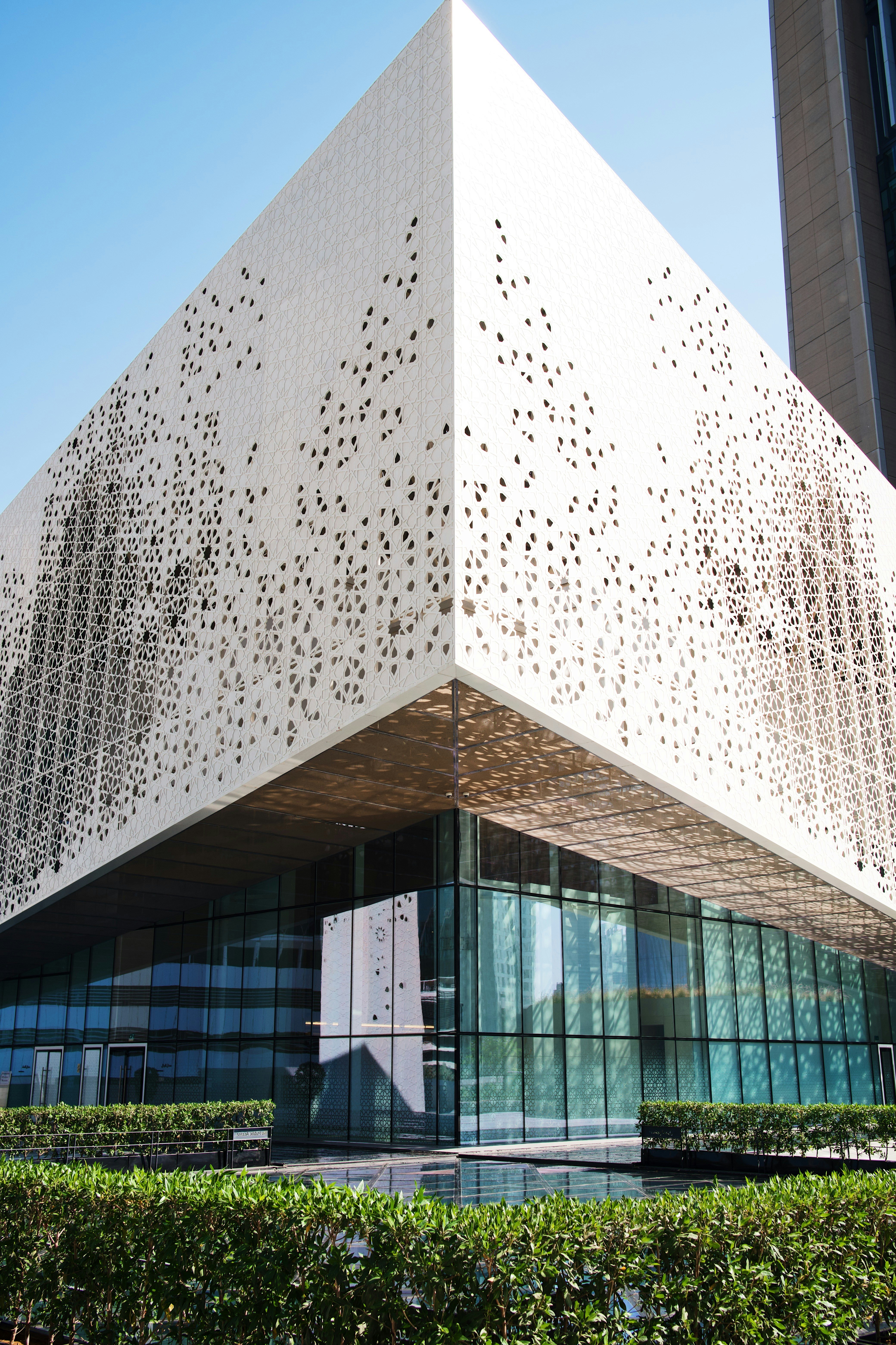 Vertex of Light: Perforated White Facade Framing Glass and Hedge