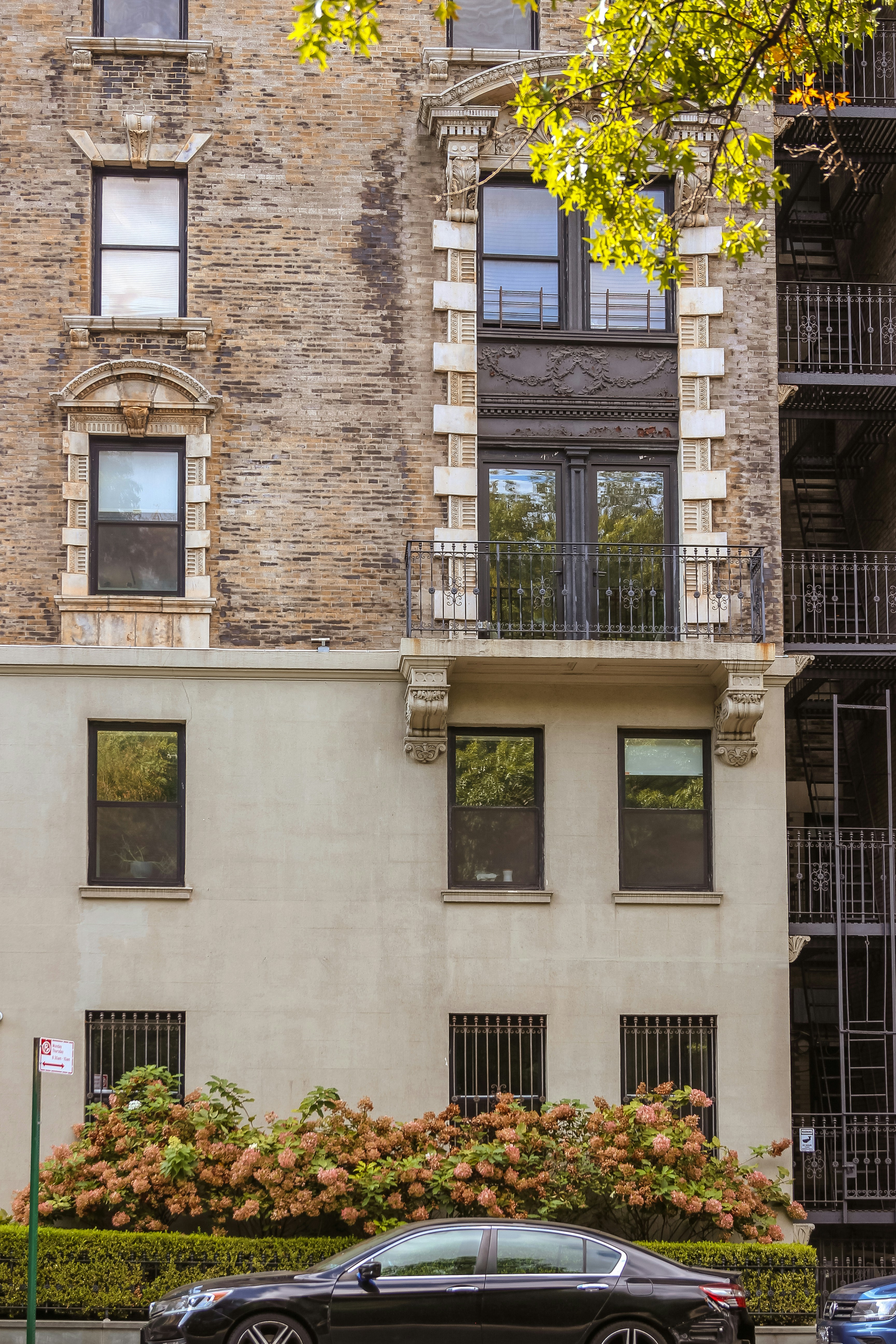 Historic brick building facade juxtaposed with modern elements, featuring intricate detailing and lush greenery at the base.