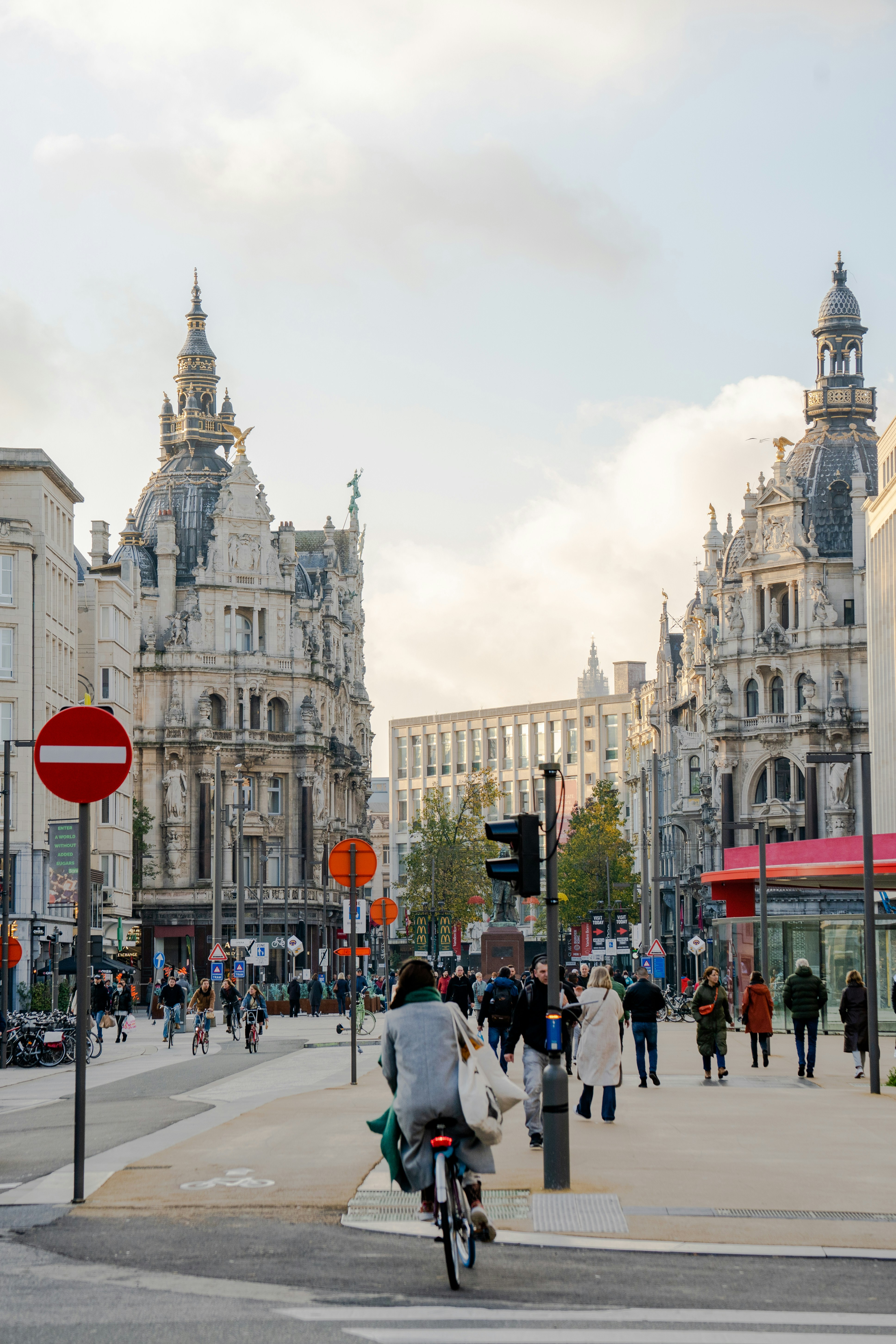 View down a busy street in Antwerp, Belgium | a man riding a bike down a street next to tall buildings