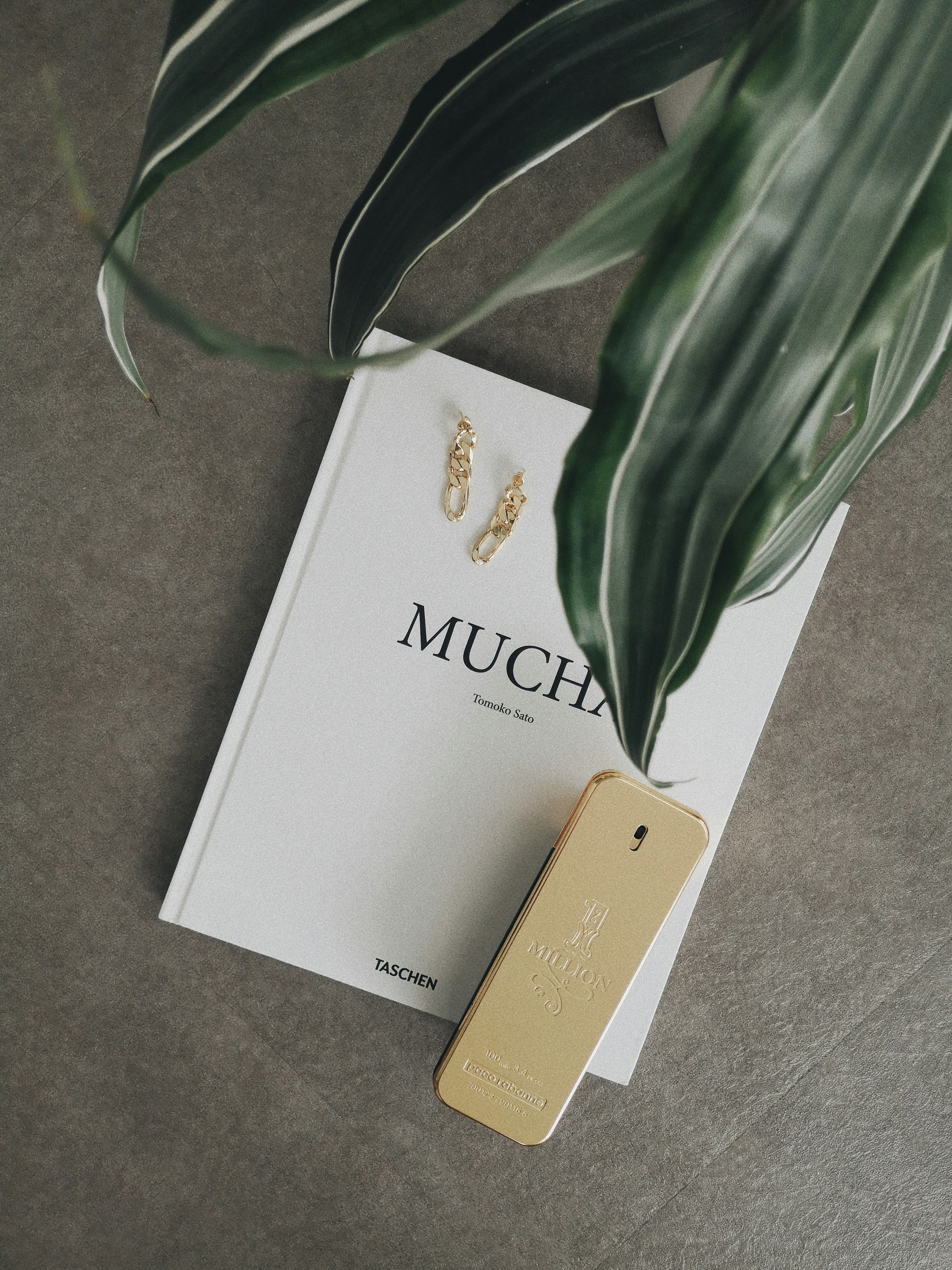 One million by Paco Rabanne perfume on a white art book of Mucha work and gold earrings.