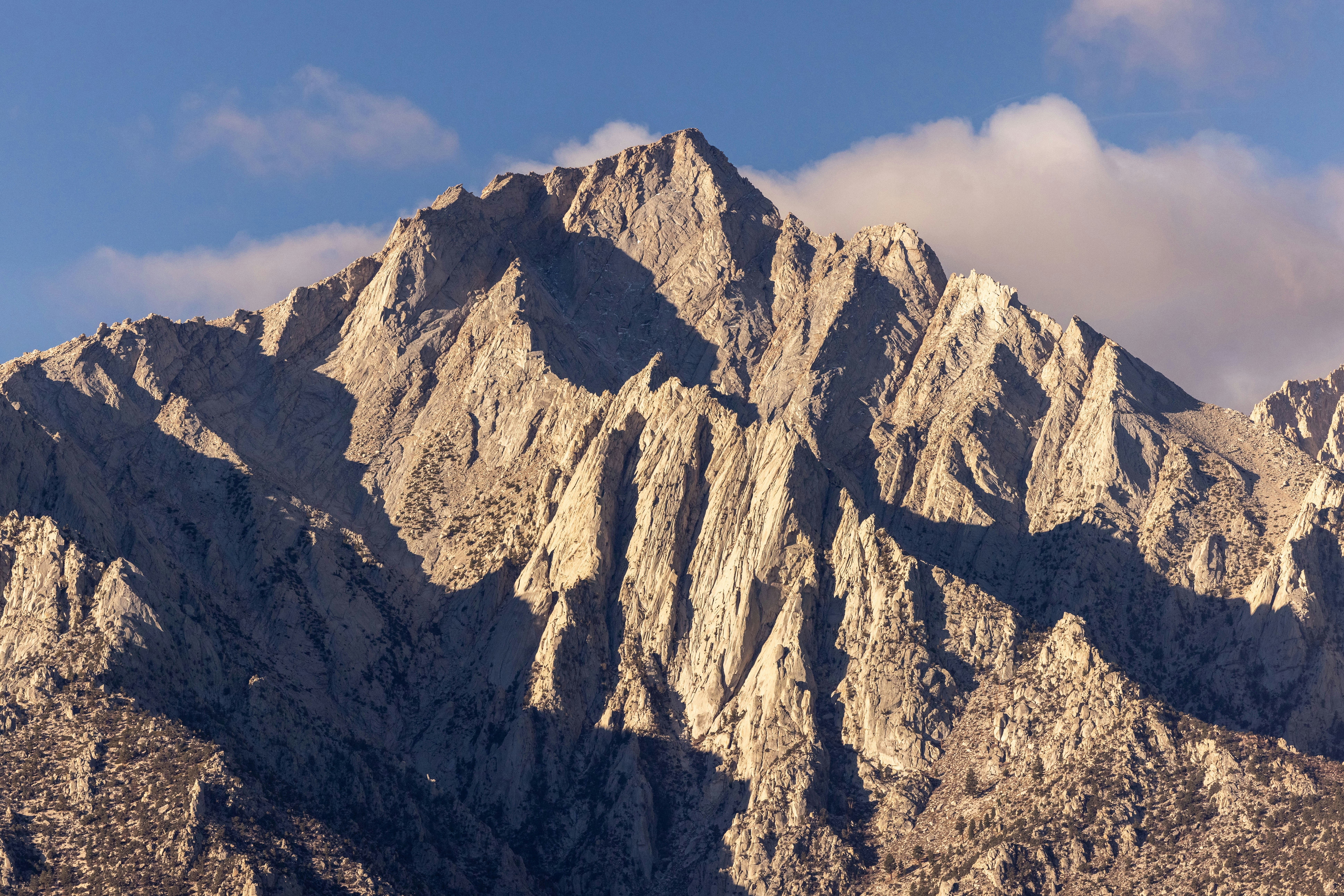 Majestic mountain range showcasing jagged peaks and intricate rock formations under a soft sky. The play of light and shadow accentuates the rugged texture of the landscape.