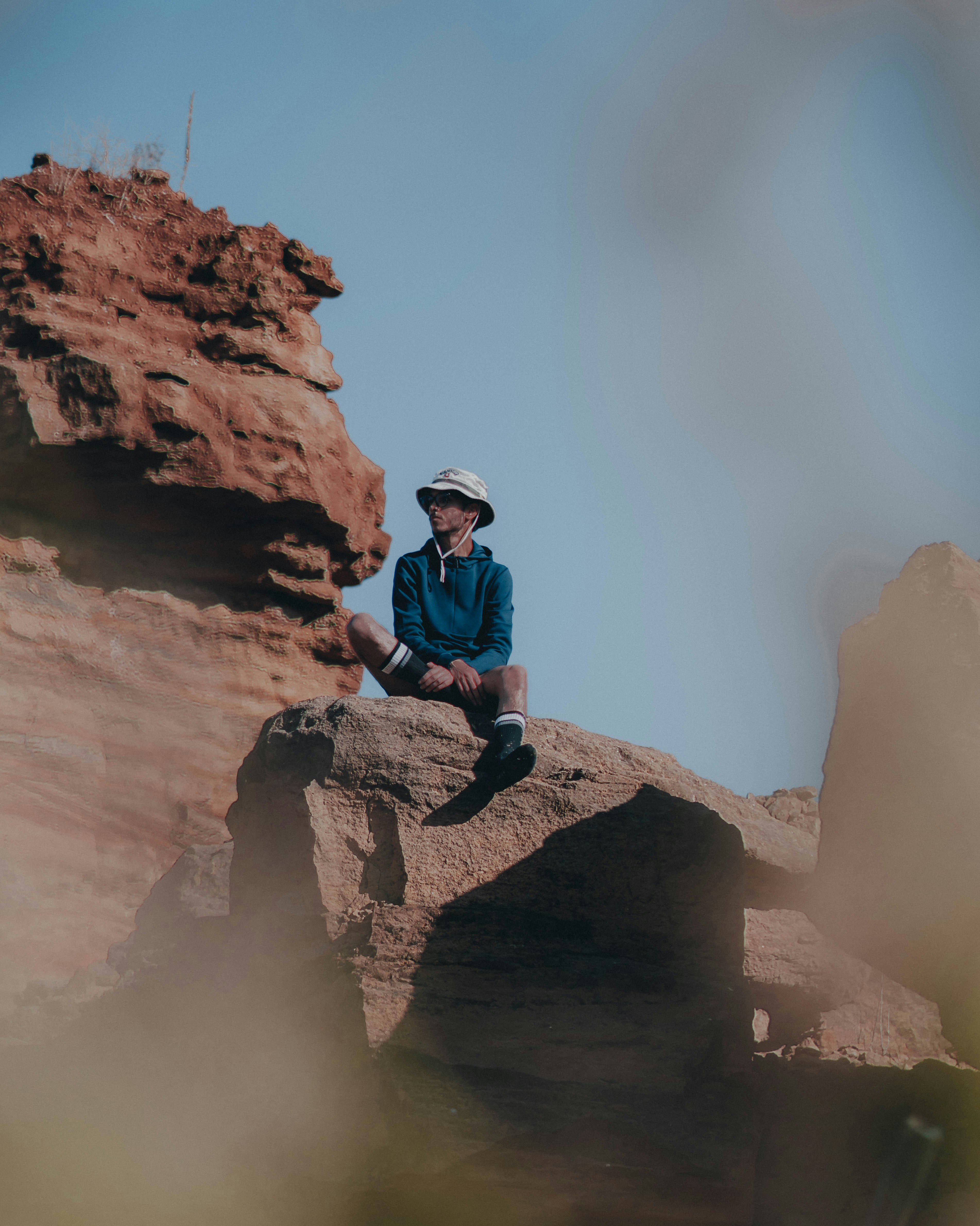 A person sitting thoughtfully on a rocky outcrop, surrounded by natural formations under a clear blue sky.