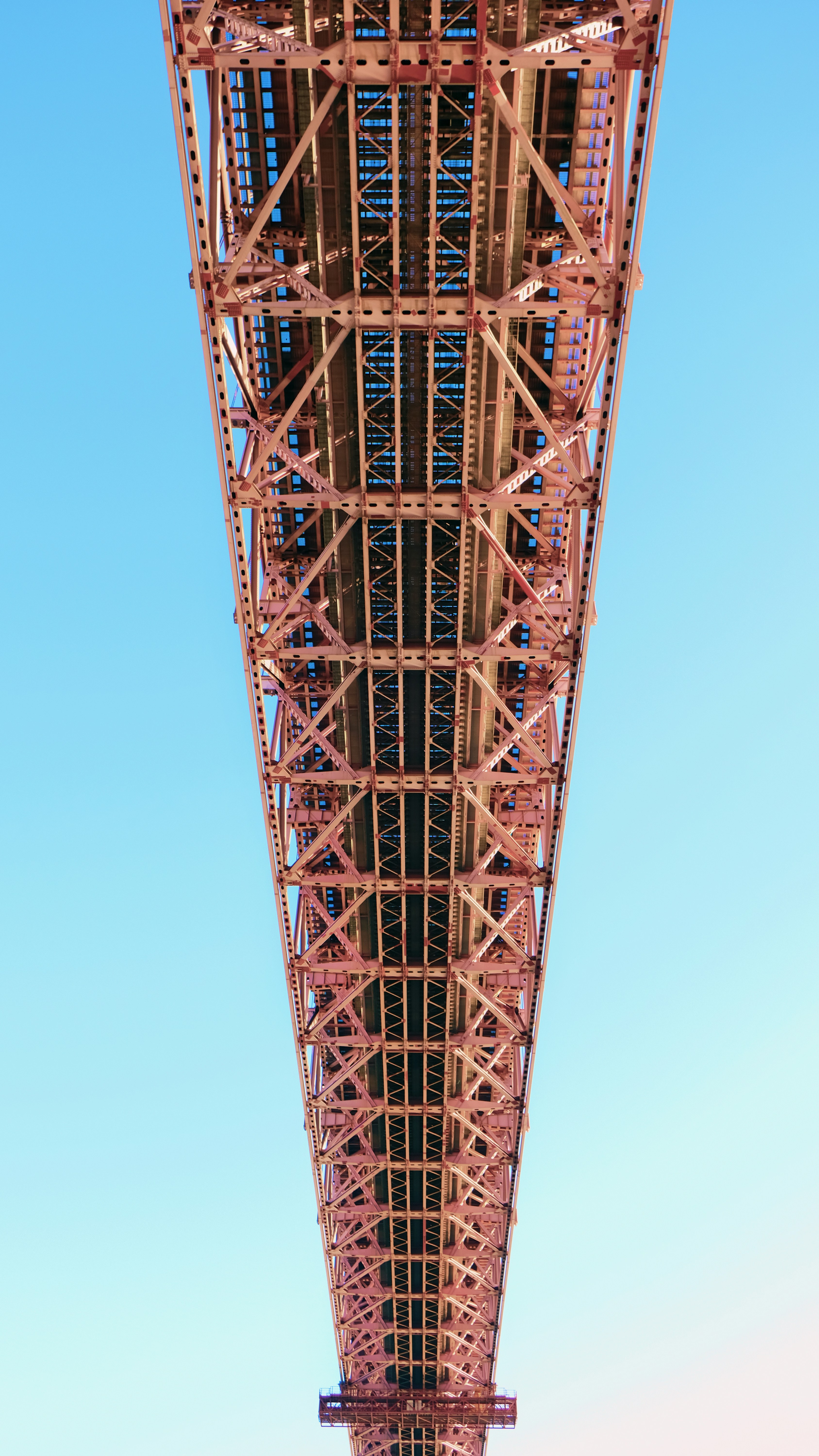Intricate steel framework of a bridge captured from below against a clear blue sky.