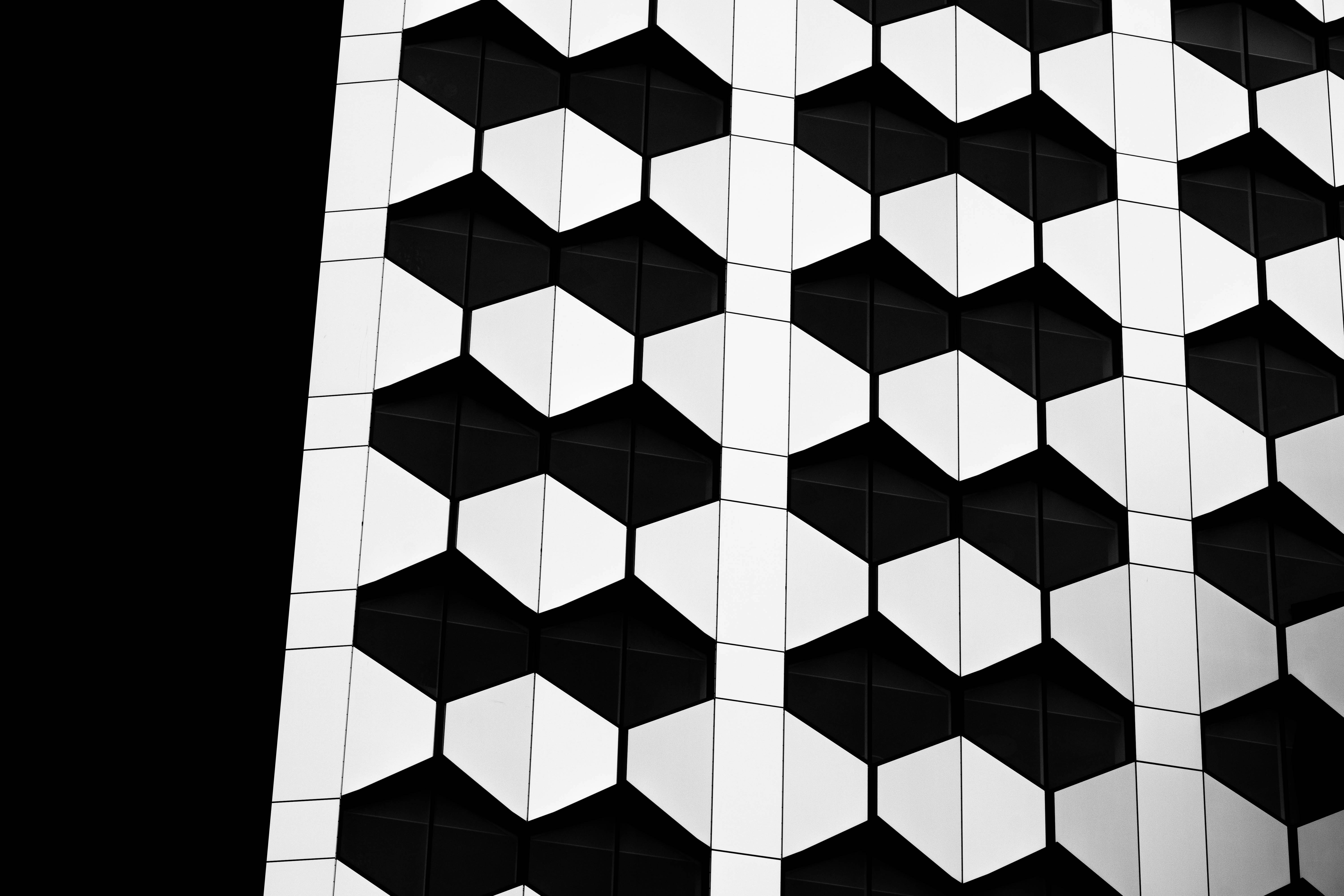 Abstract architectural design featuring a pattern of hexagonal shapes in contrasting black and white. The interplay of light creates a dynamic visual effect.