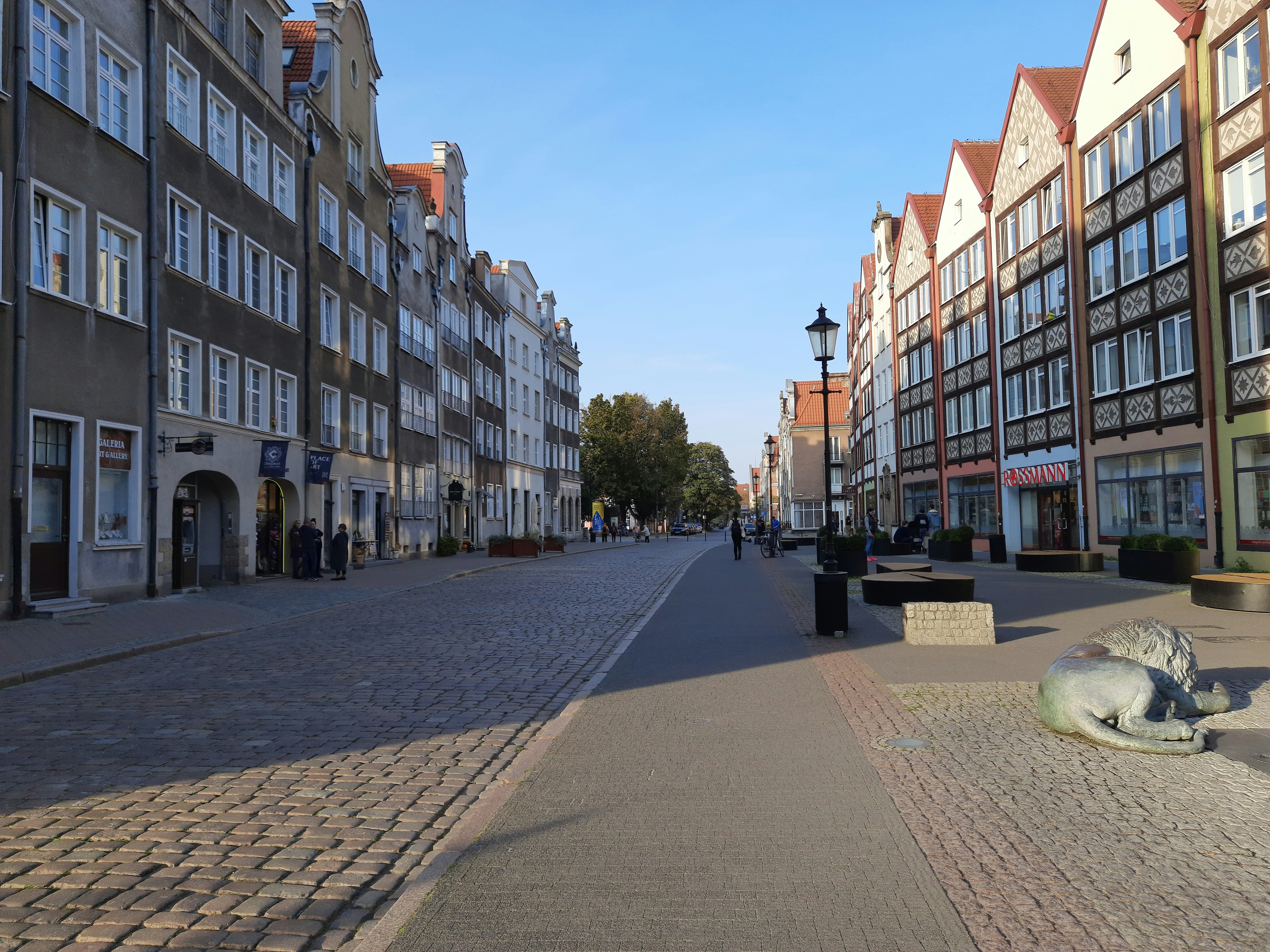 Sunlit cobblestone street flanked by traditional European townhouses under a clear blue sky.