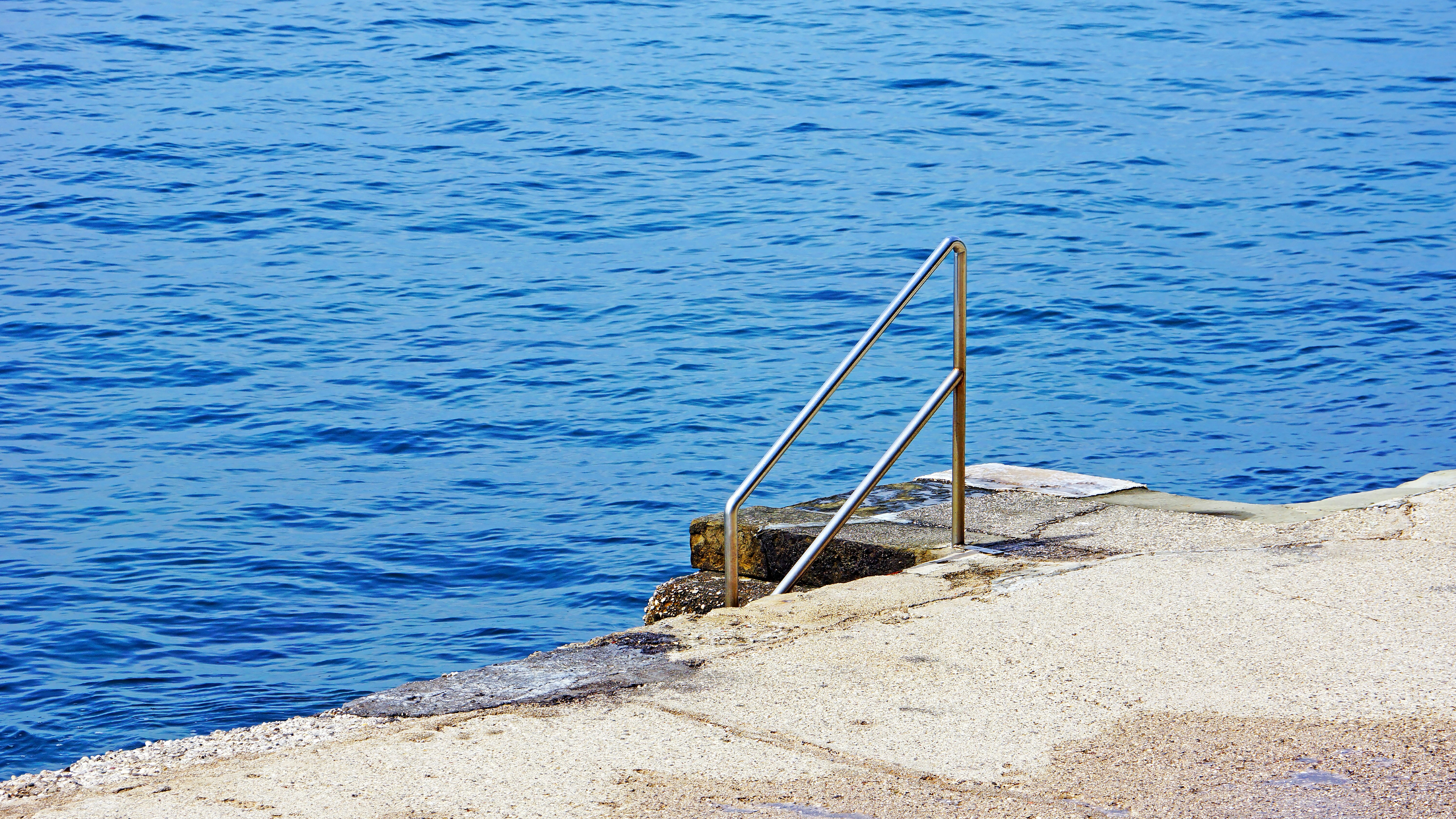 A railing on the edge of a body of water photo – Free Beach Image on ...