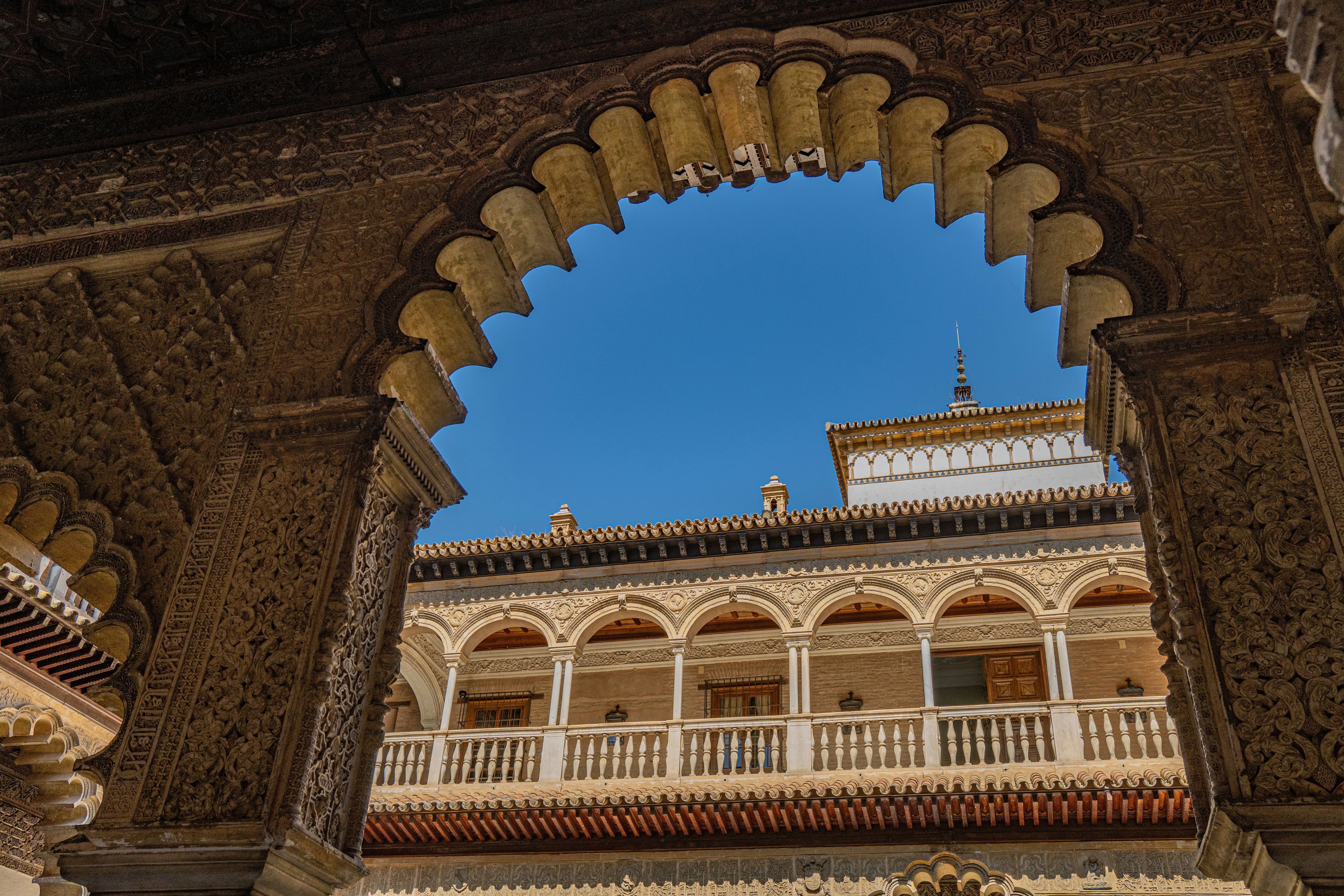Ornate stone archway frames a view of a historic courtyard under a clear blue sky.
