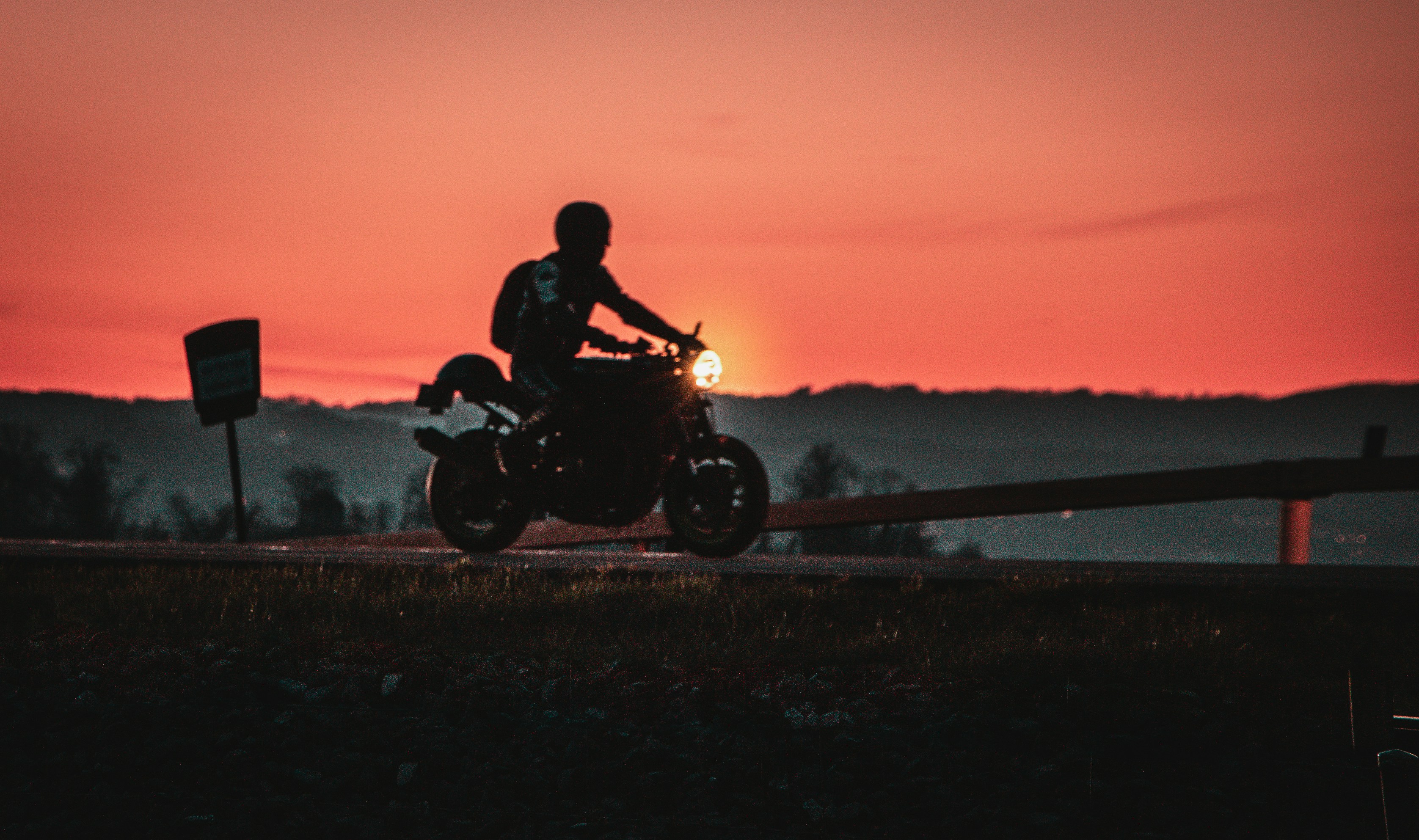 Silhouetted motorcyclist cruising along a winding road against a vibrant sunset backdrop.