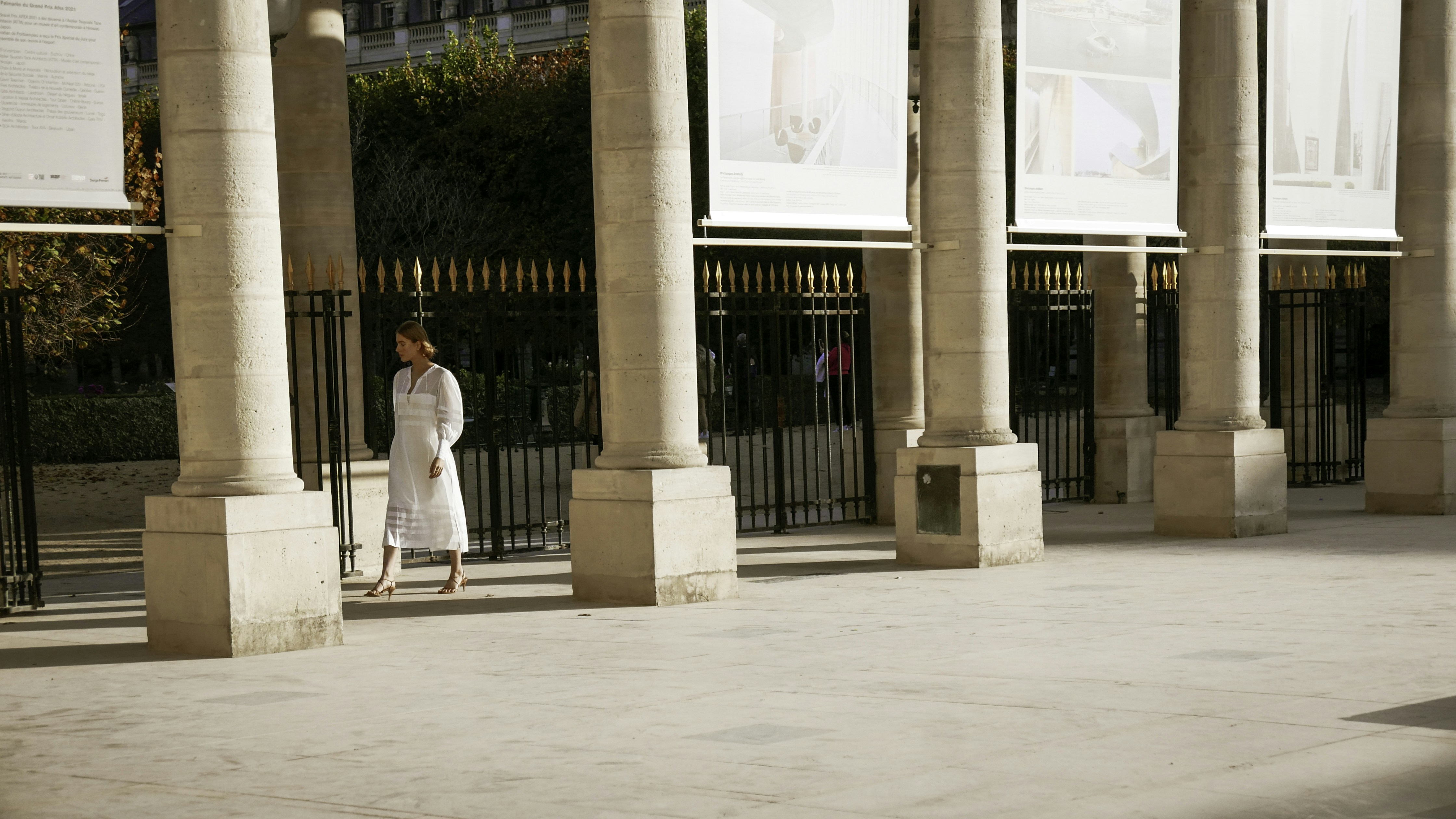 Figure in white walking between colonnades under banners