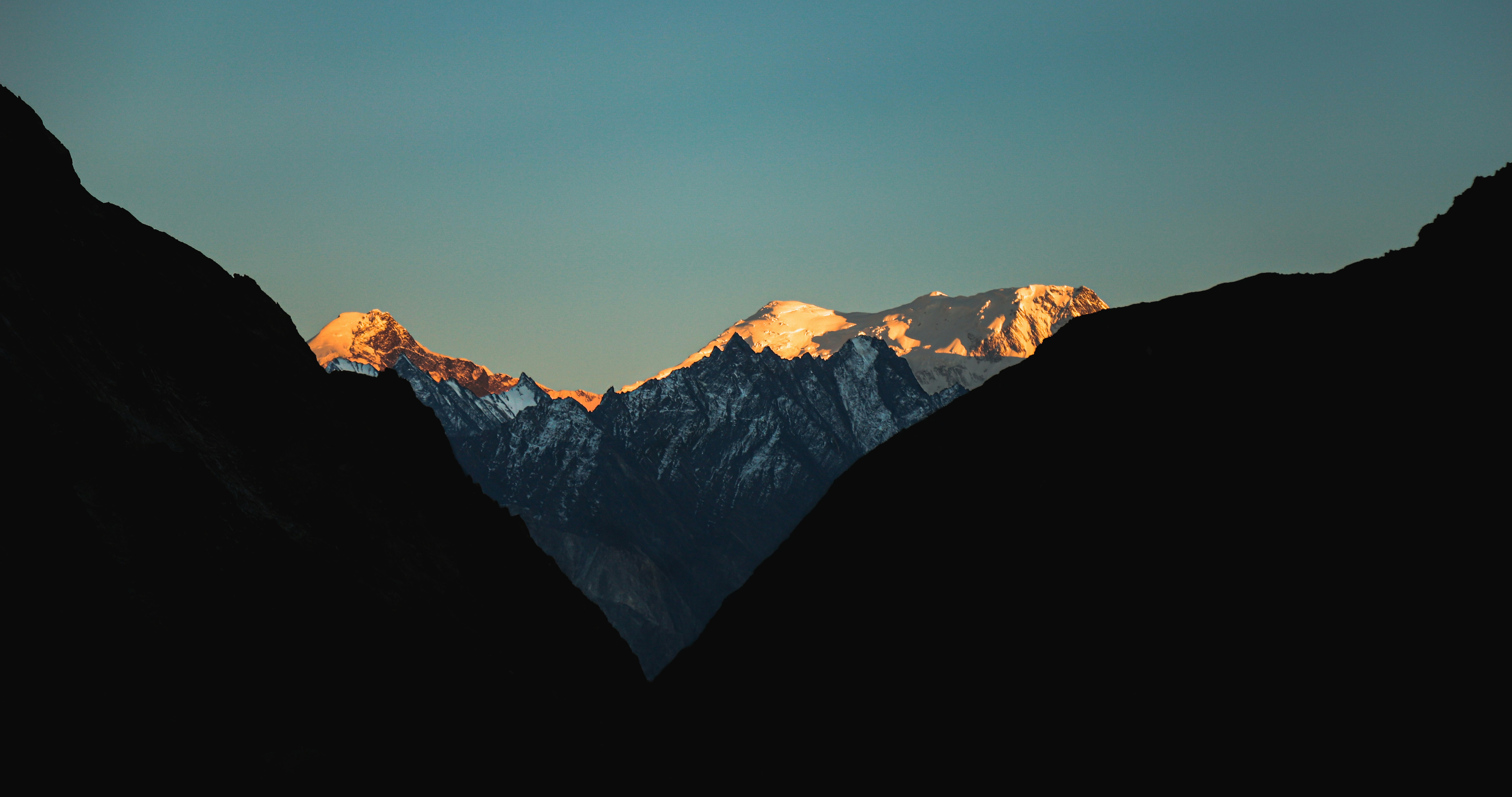 Snow-capped mountains glowing in sunset light between darkened valley silhouettes.