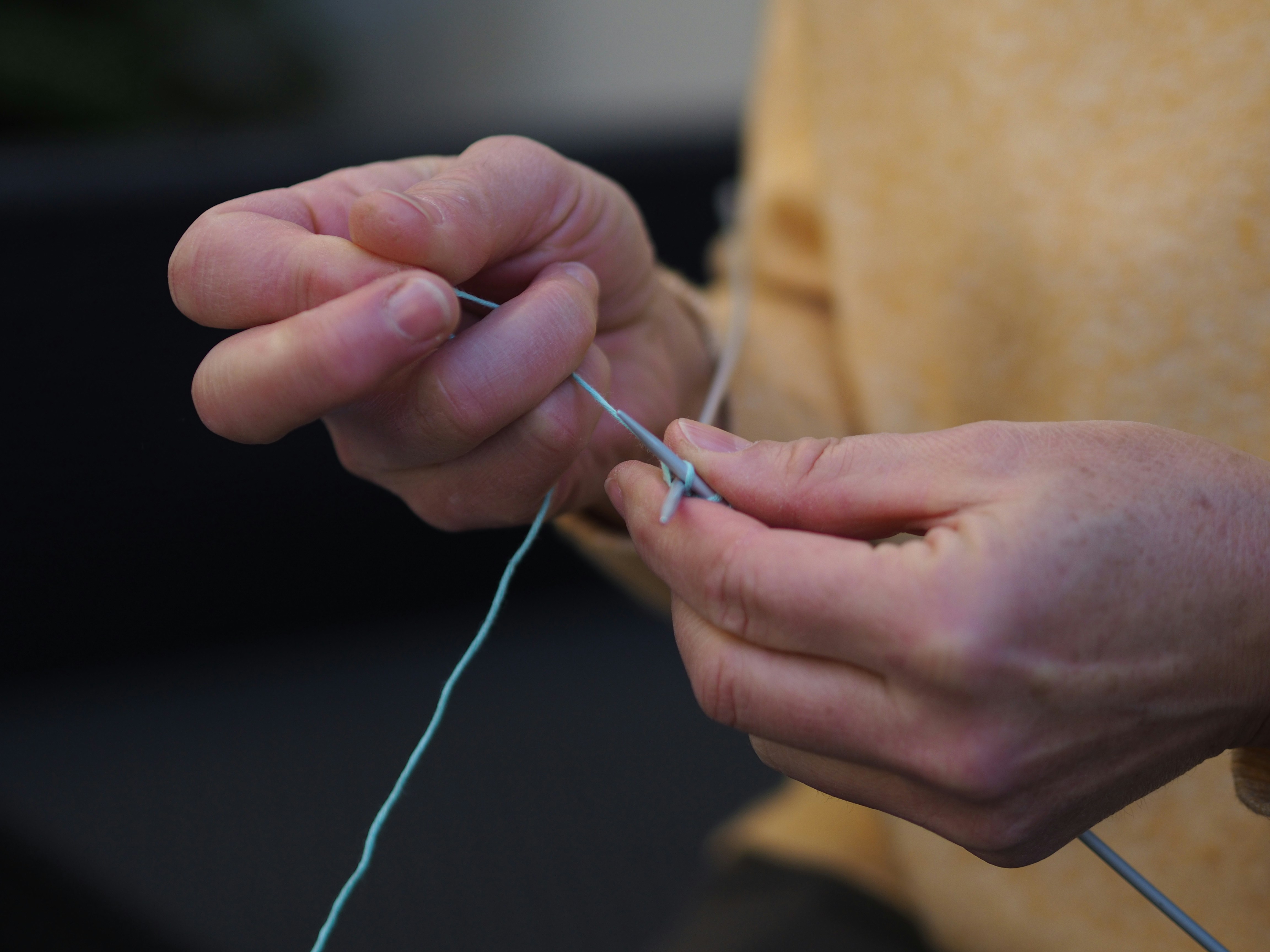 Hands skillfully threading a light blue string through a needle, showcasing the art of crafting. The focus is on the intricate details of the hands and the materials used.