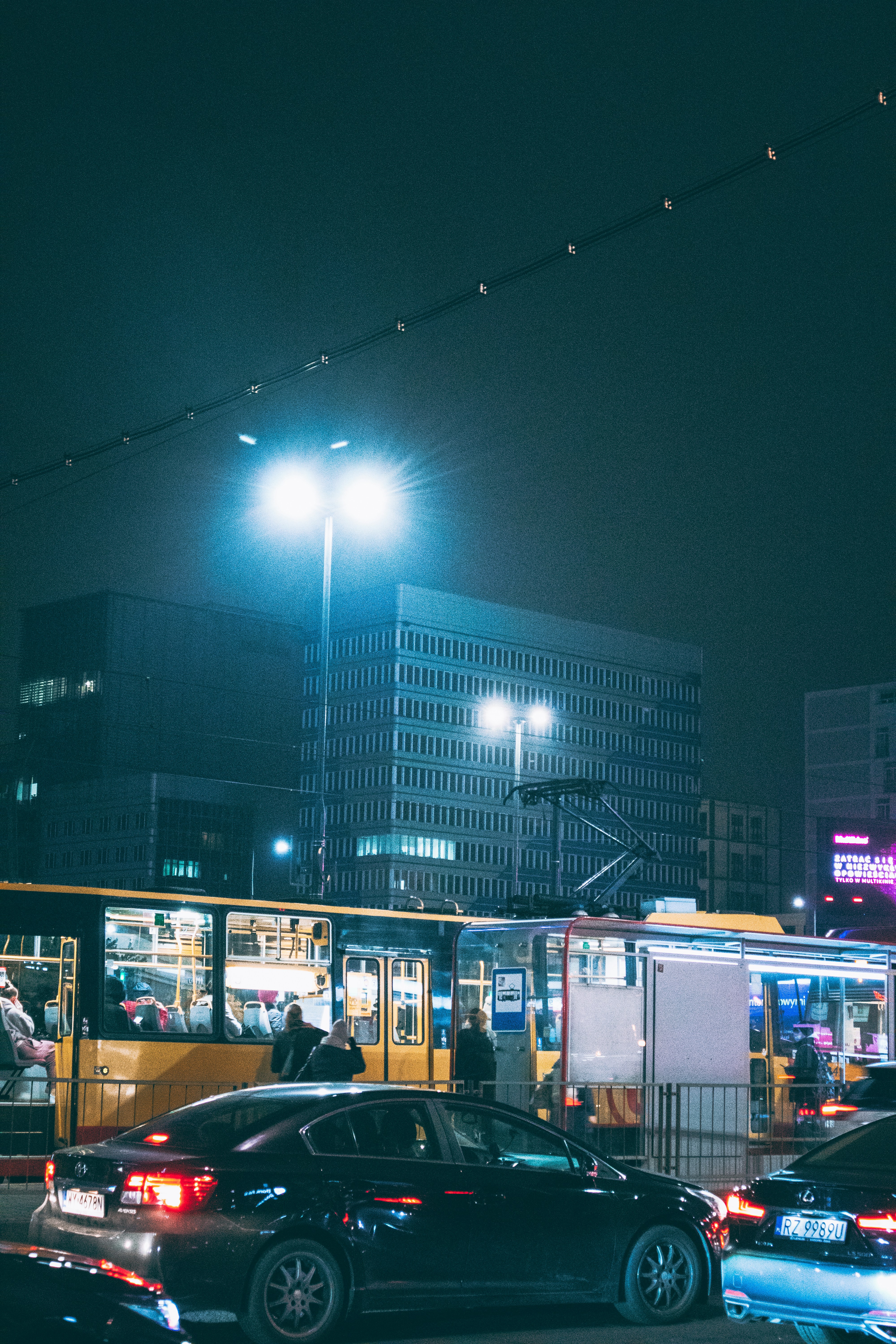 Illuminated tram navigating through a bustling city intersection at night, surrounded by modern architecture and traffic. 