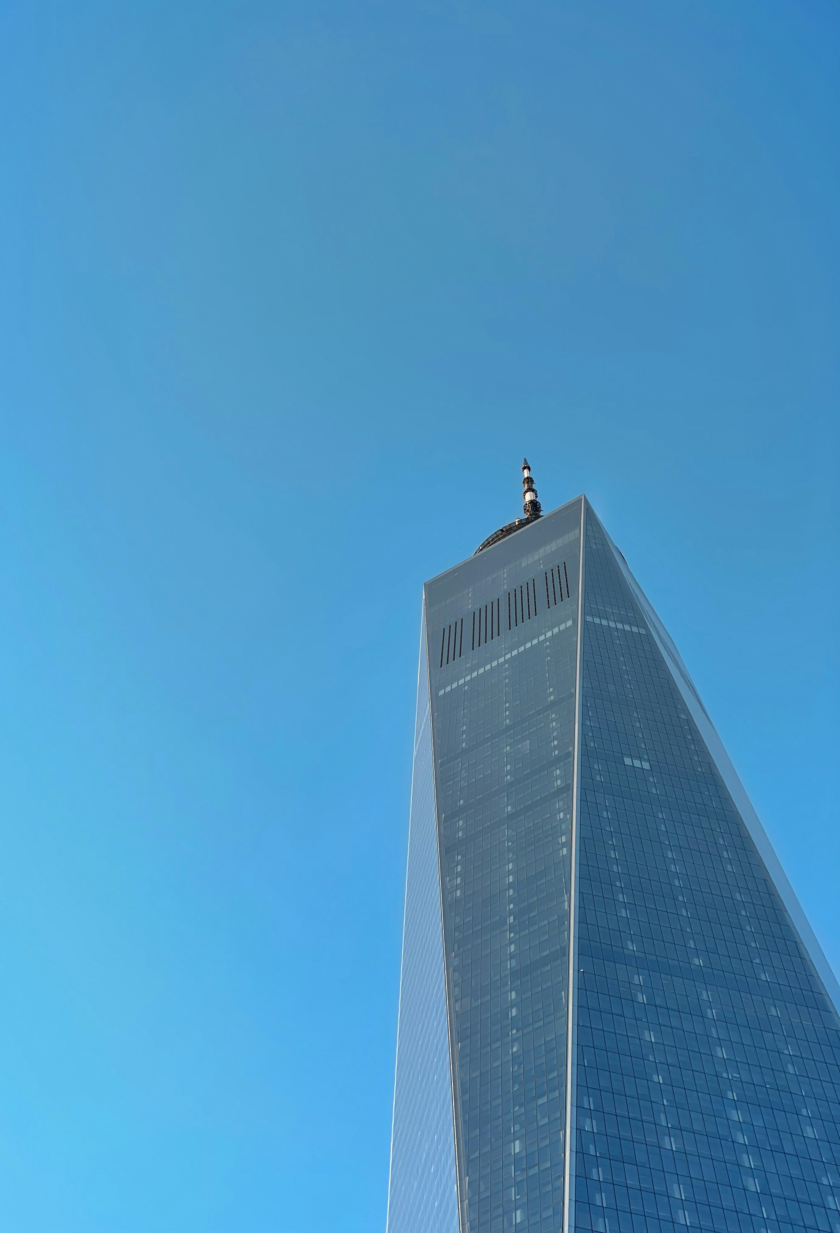 The One World Trade Center rises majestically against a clear blue sky, showcasing its sleek glass façade and intricate architectural design.