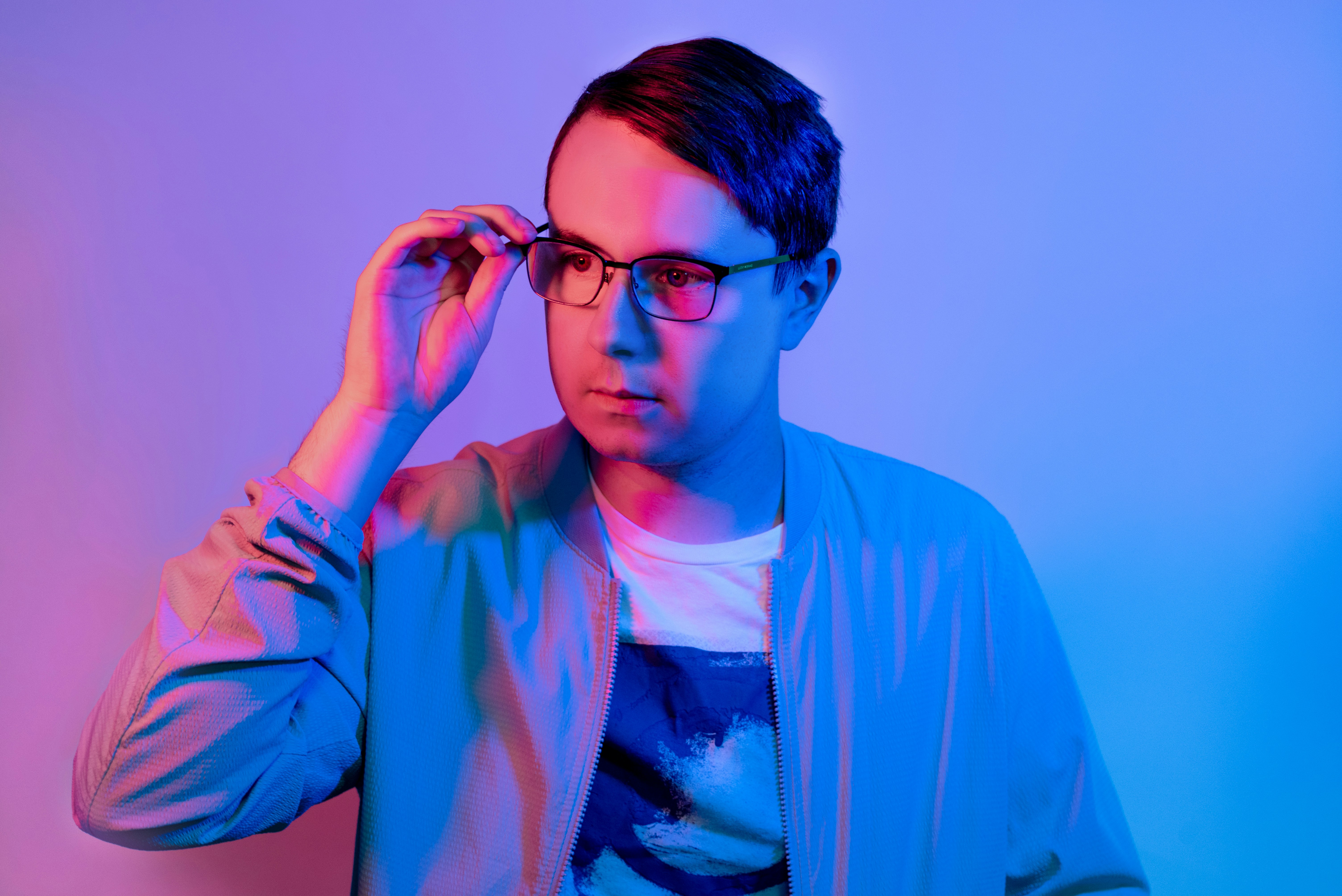 Person adjusting glasses in a studio lit with vibrant blue and pink hues.