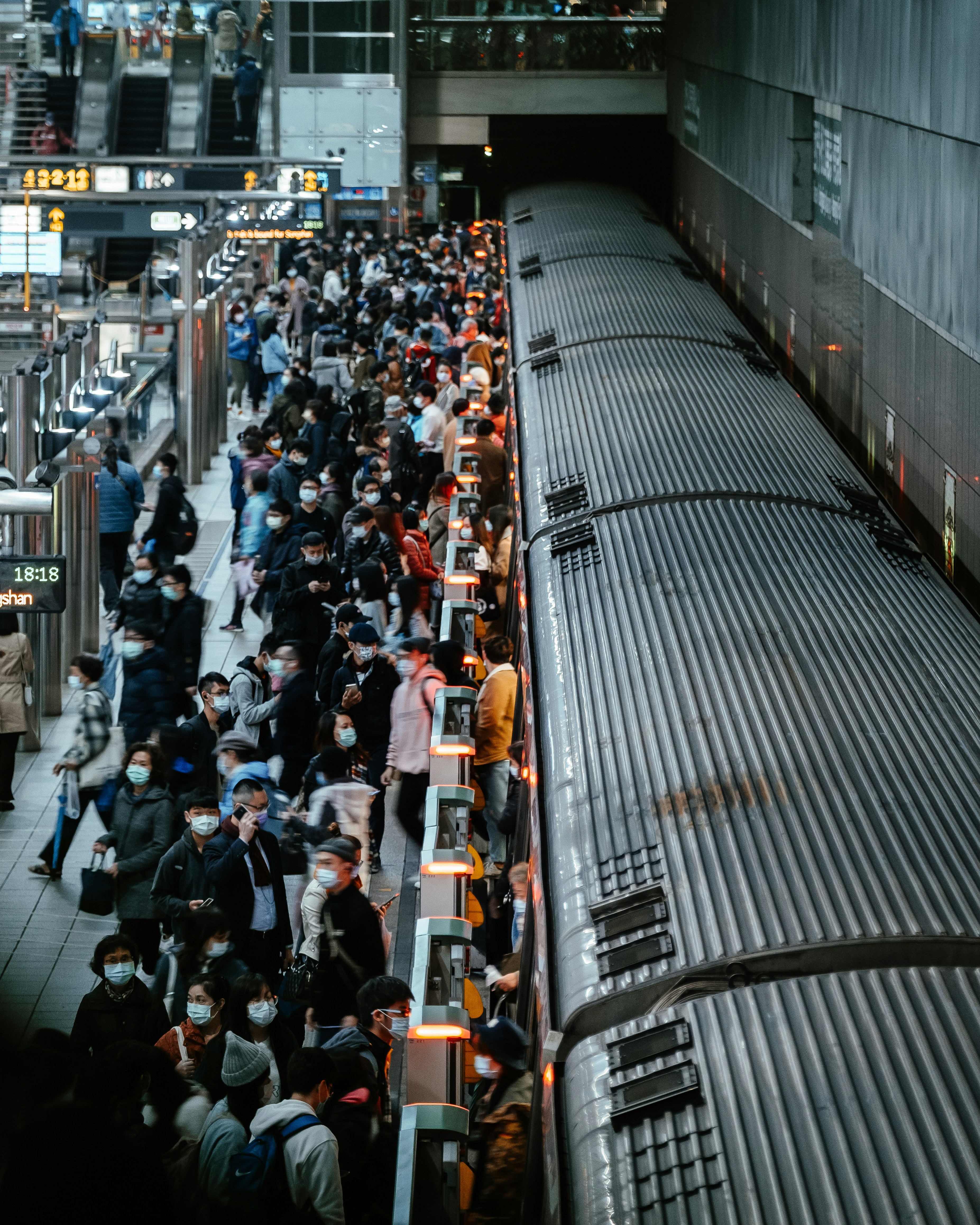 Crowd of commuters waiting at a bustling train station, illuminated by warm platform lights. The scene captures the essence of urban life in motion.