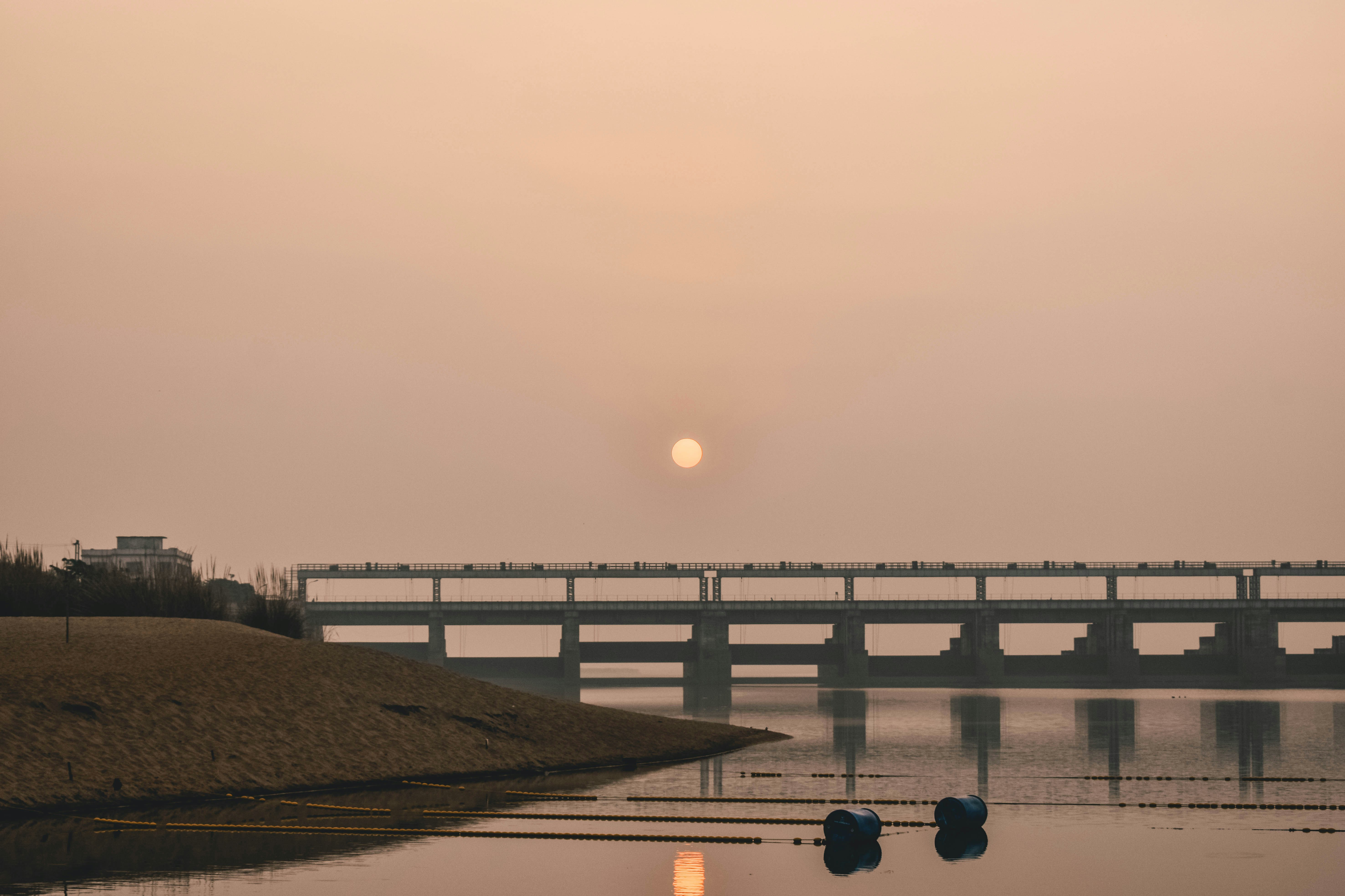 the sun is setting over a bridge over a body of water
