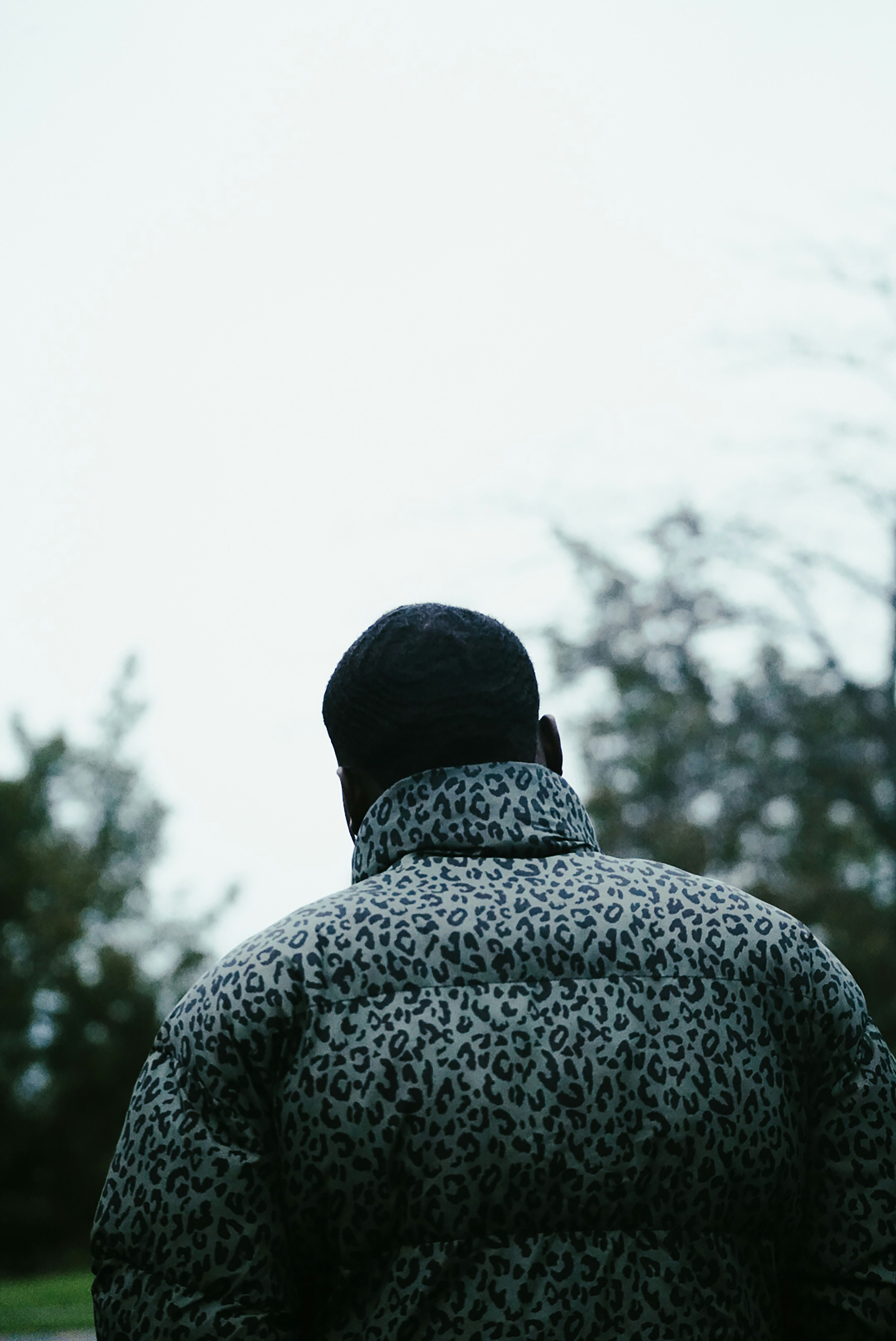 Individual in a leopard-print puffer jacket gazing into the distance, surrounded by nature's muted tones.