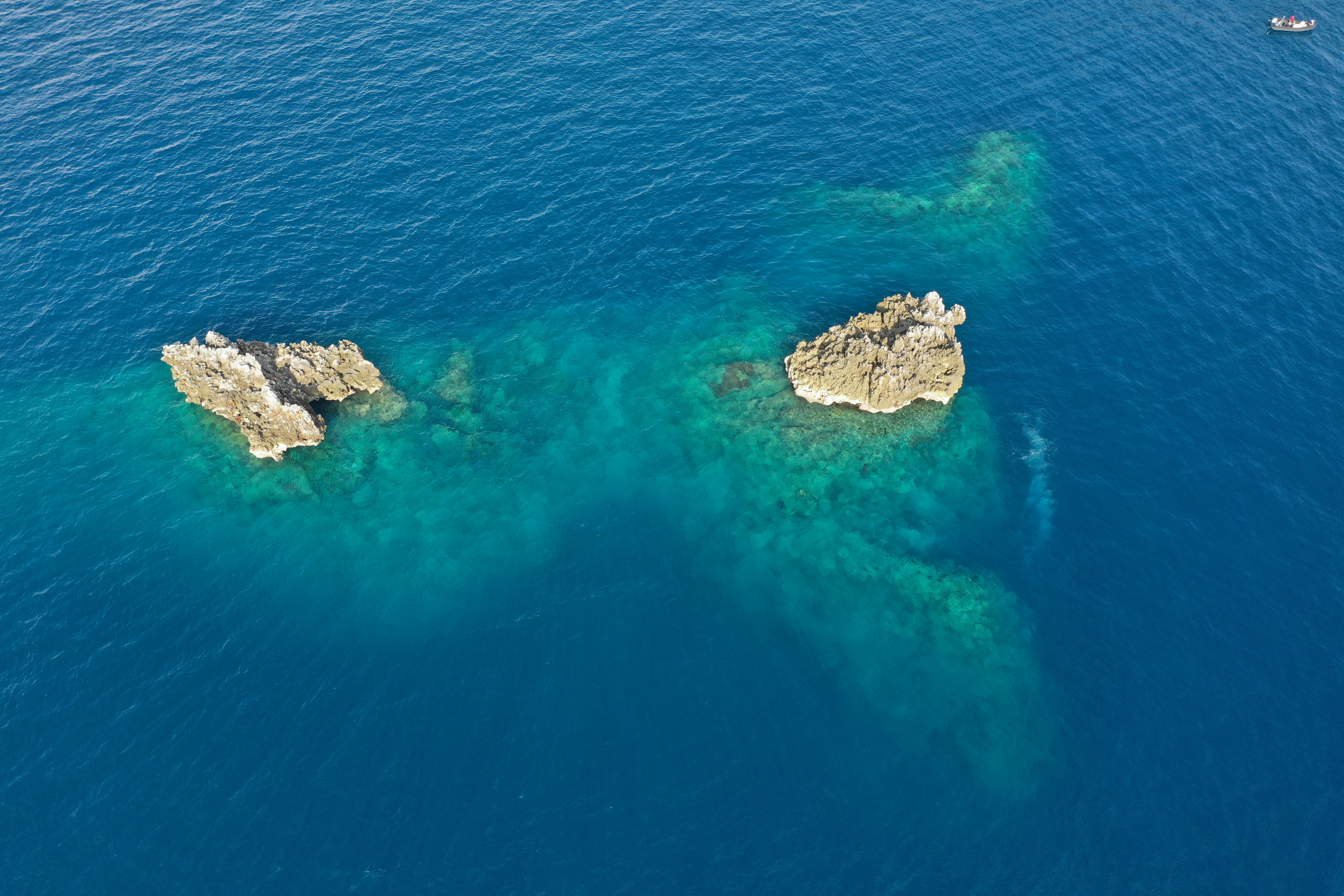 Two rugged rock formations emerge from the deep blue sea, surrounded by vibrant turquoise waters, showcasing the contrast between land and ocean.