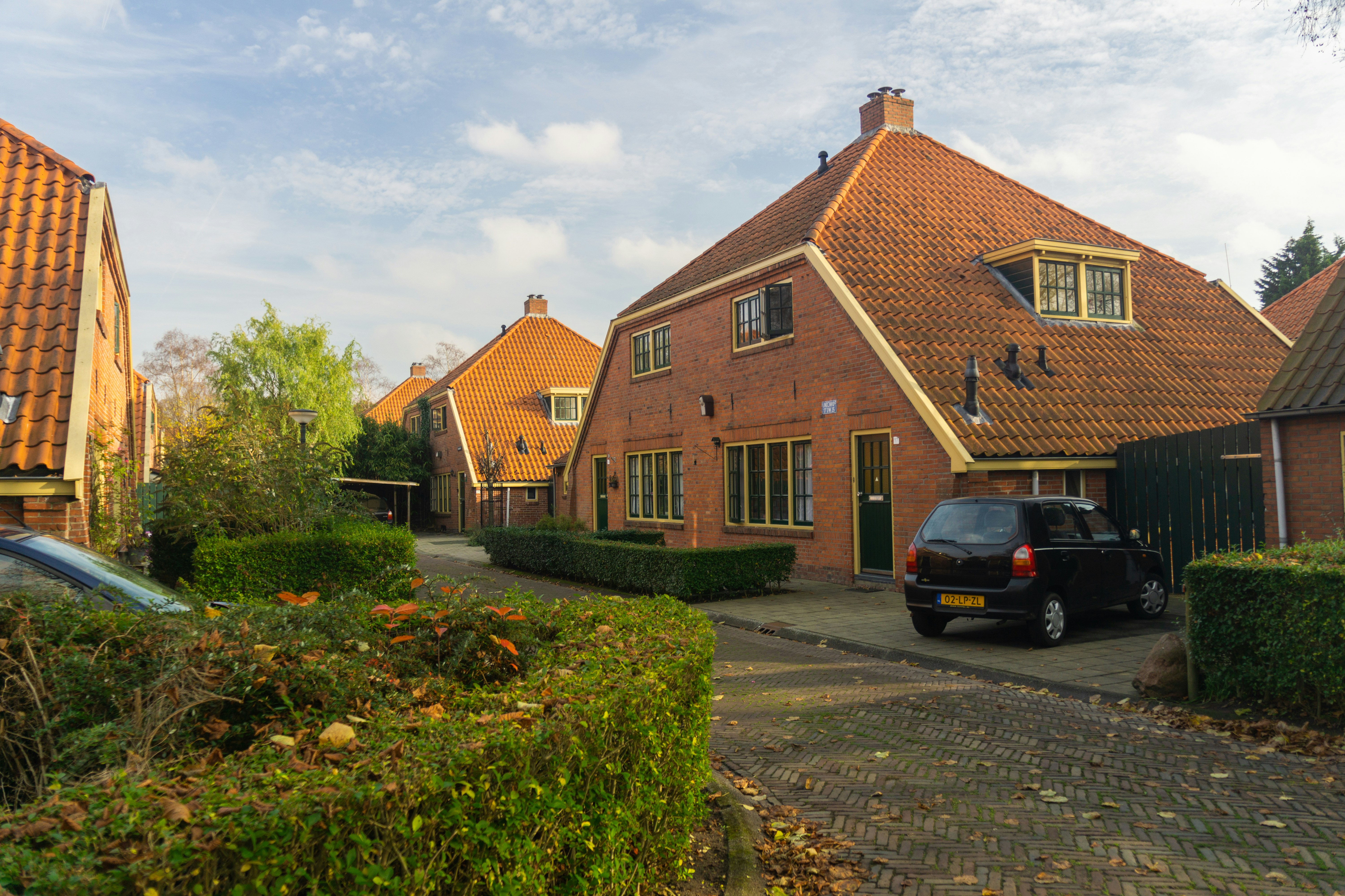 Charming brick houses with steep roofs along a quiet suburban street under a partly cloudy sky.
