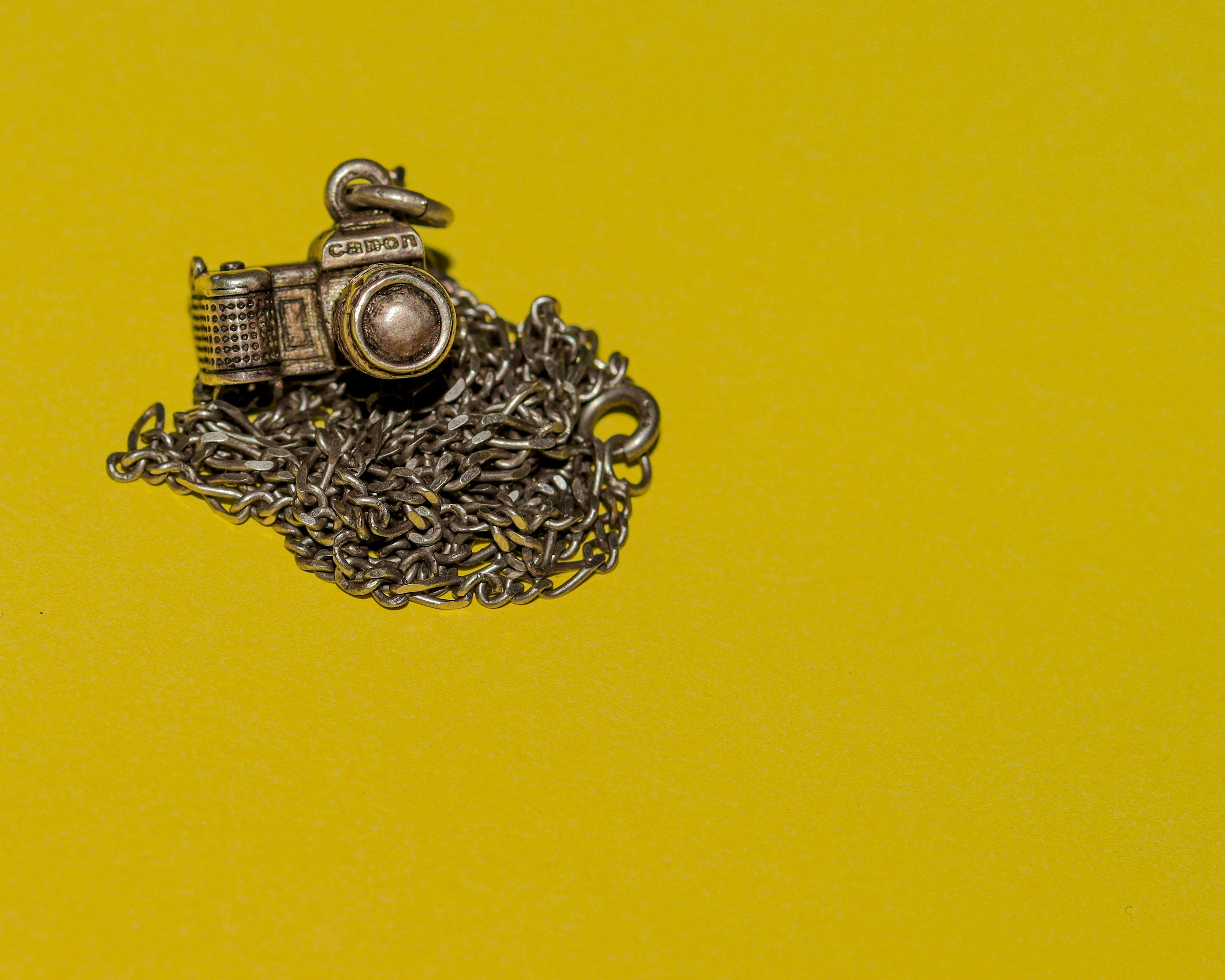 Pocket-Sized Metal Camera Pendant on a Bold Yellow Surface