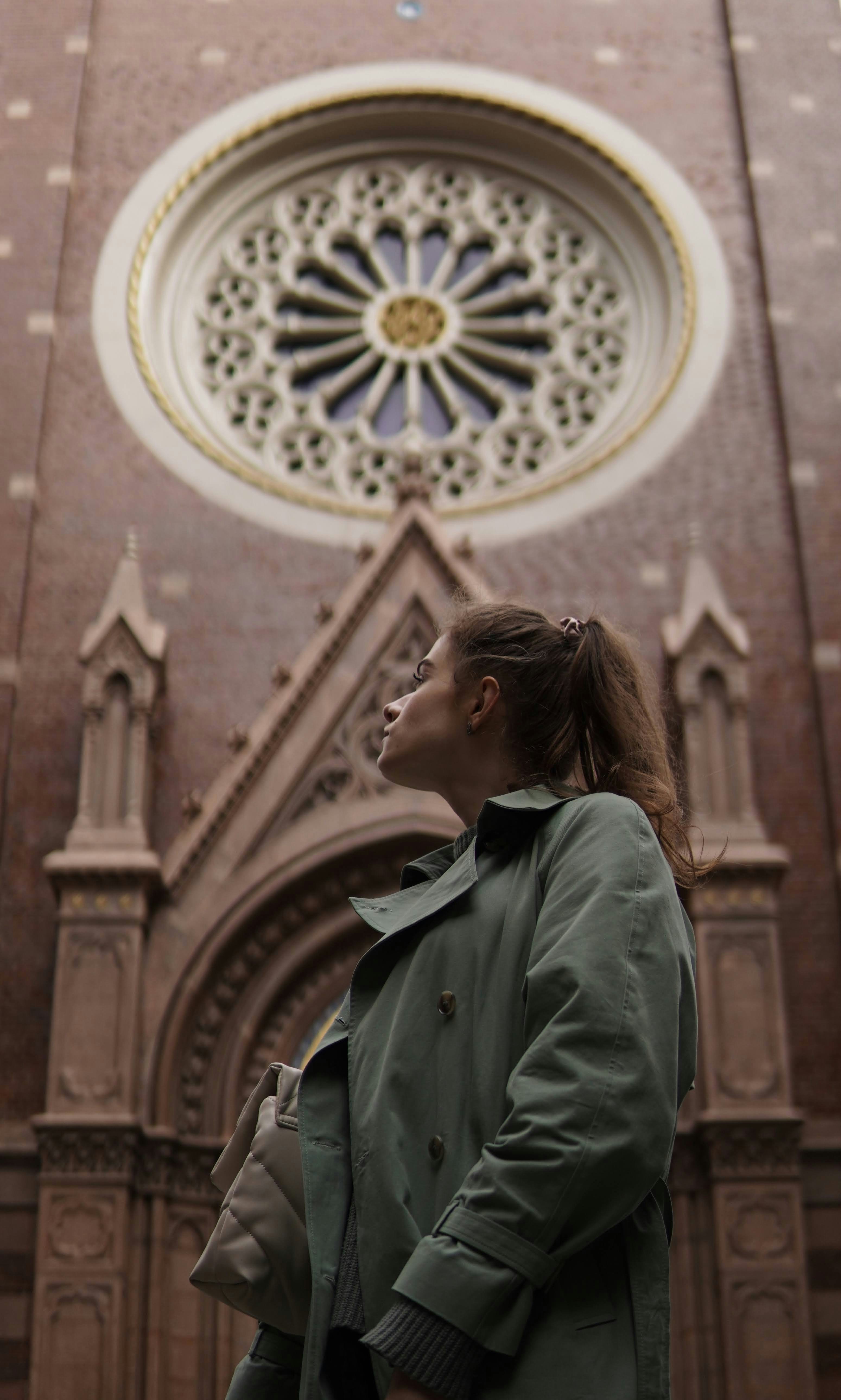 A woman gazes upward, captivated by the intricate rose window above her in a historic building. The scene highlights the interplay of human curiosity and architectural beauty.