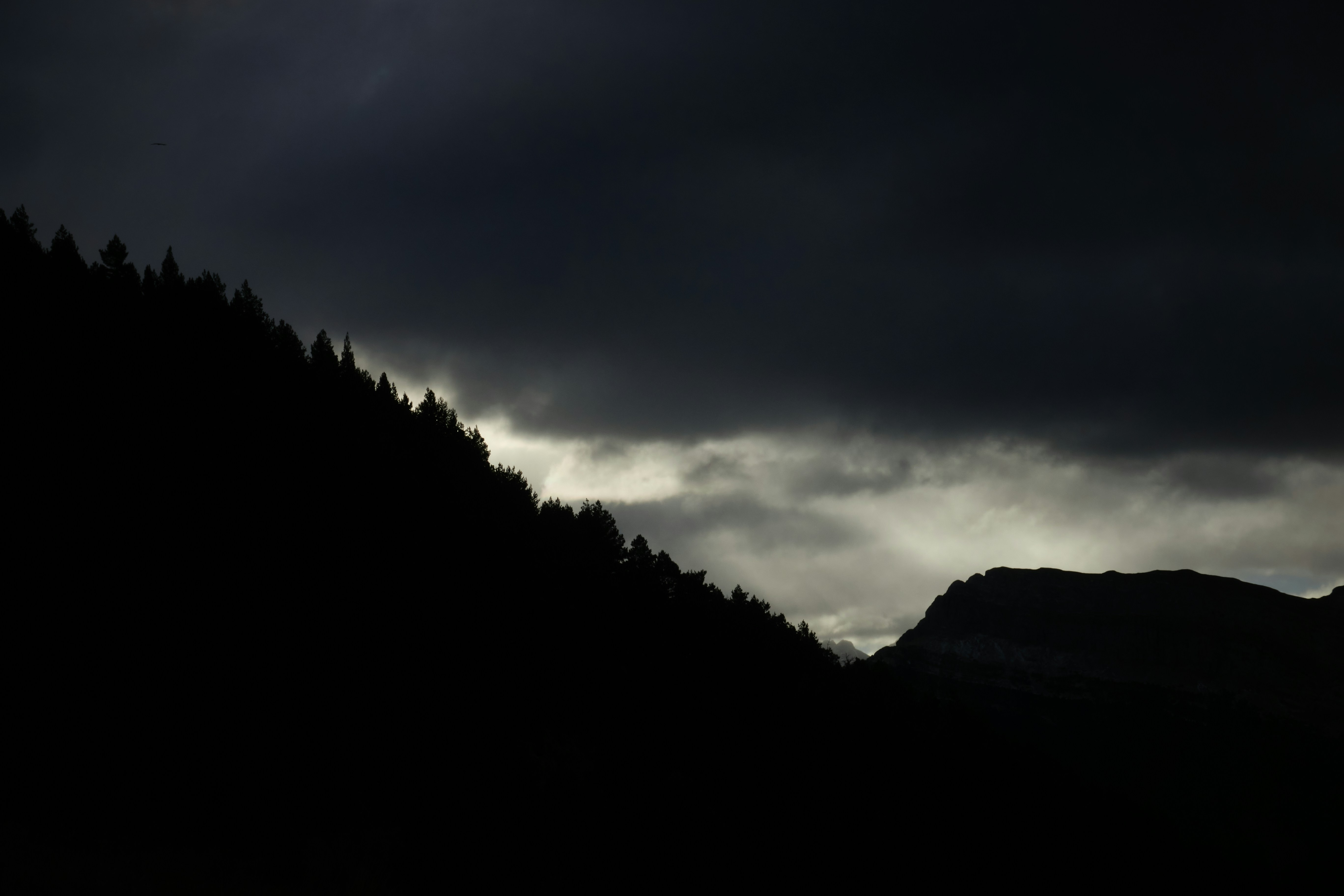Silhouetted mountain range against a dramatic sky, with clouds casting shadows over the landscape. The scene evokes a sense of mystery and tranquility.