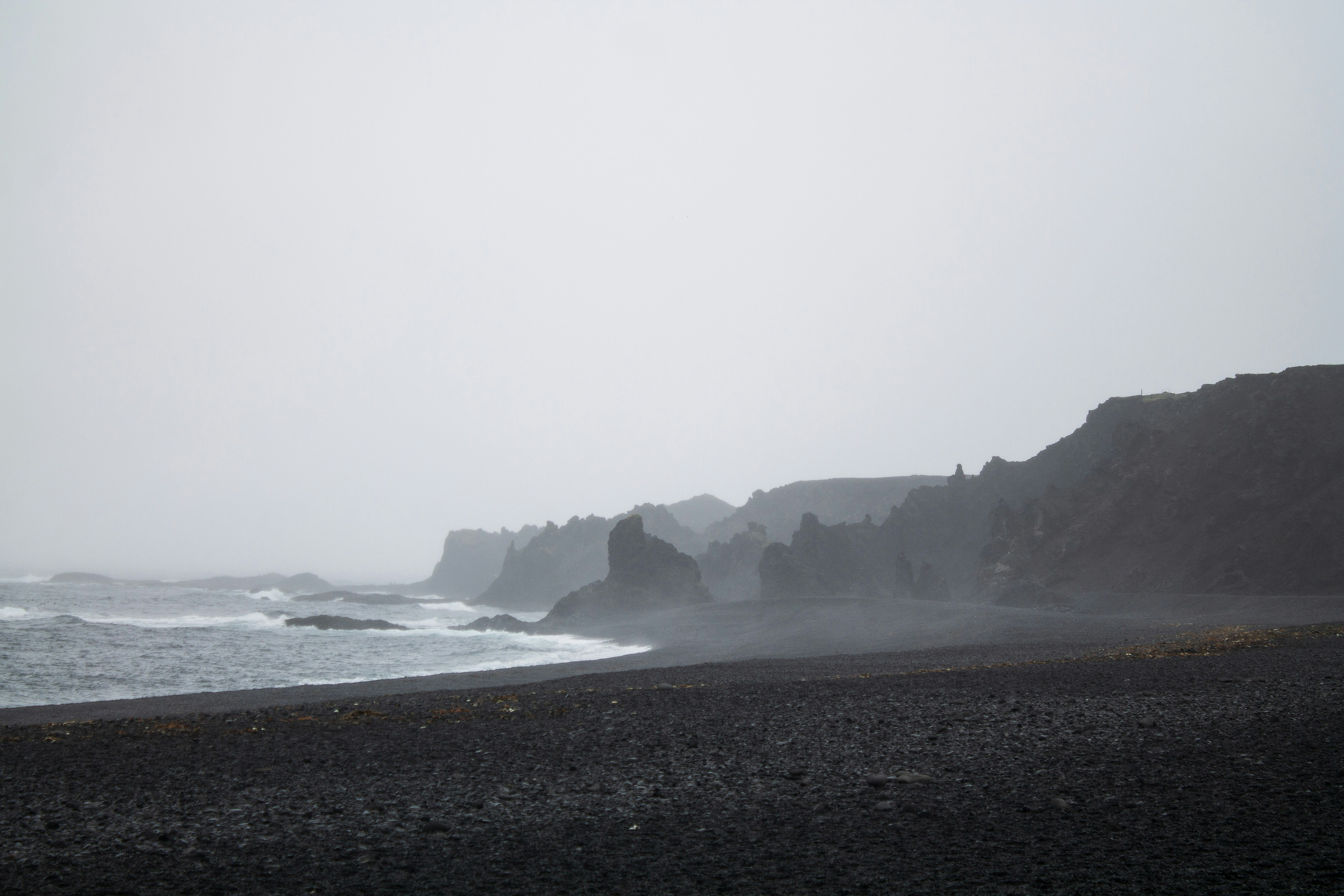 a foggy day at the beach with a black sand beach