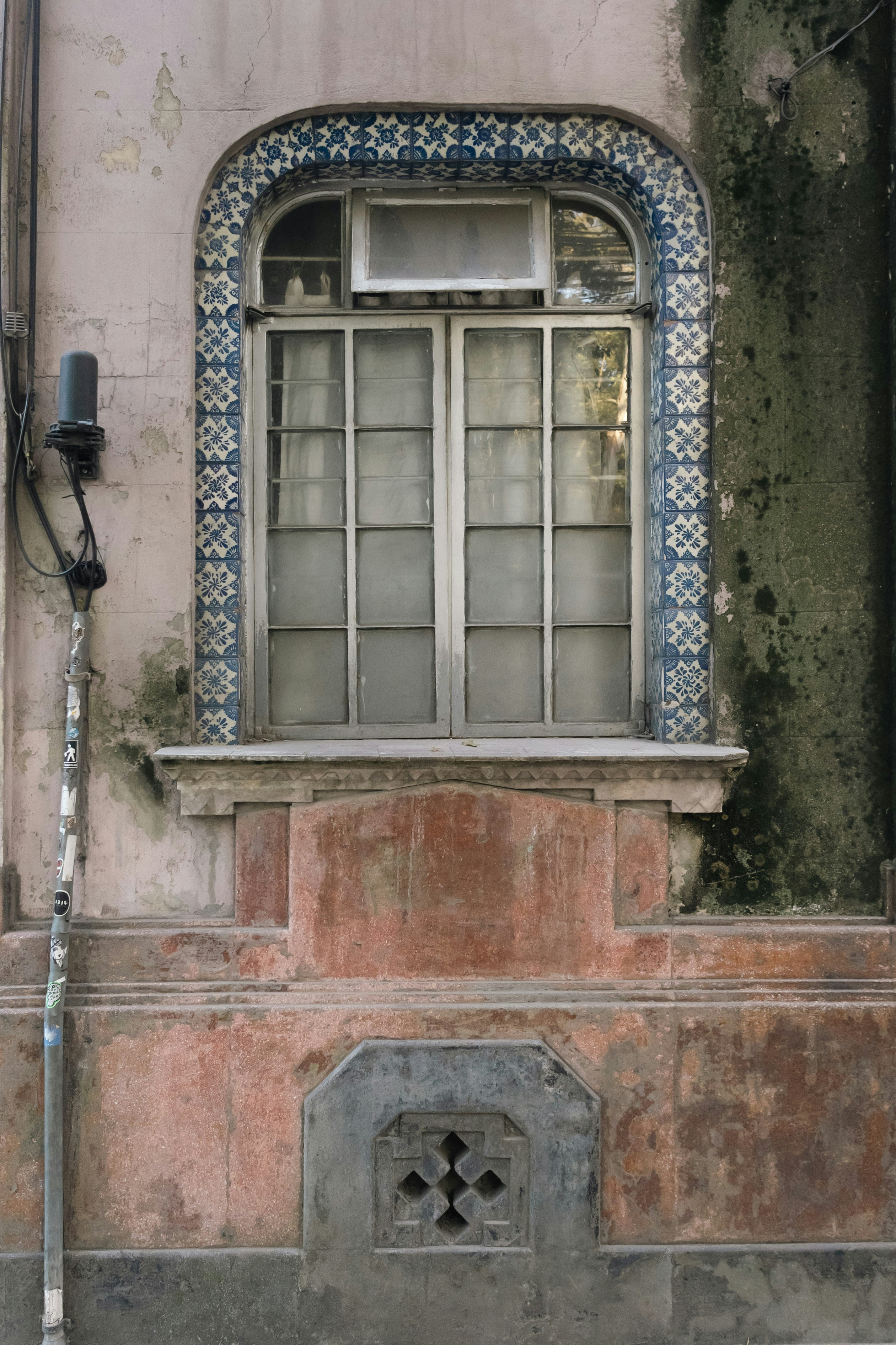 Weathered window framed by intricate tilework and peeling paint, showcasing urban decay and historical charm.