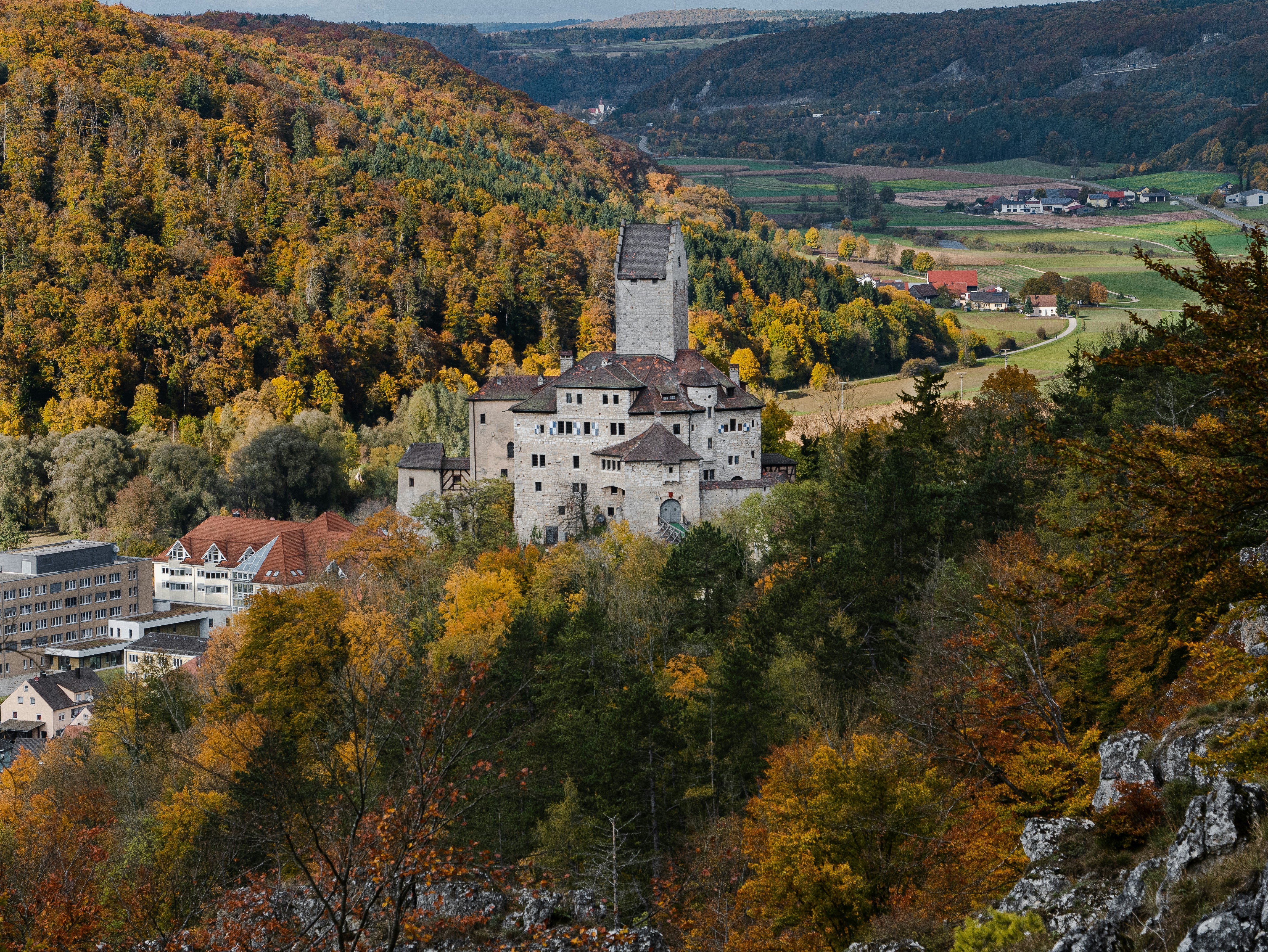 Ancient castle ruins nestled in a vibrant autumn landscape, surrounded by colorful foliage and rolling hills. The scene captures the serene beauty of nature intertwined with historical architecture.