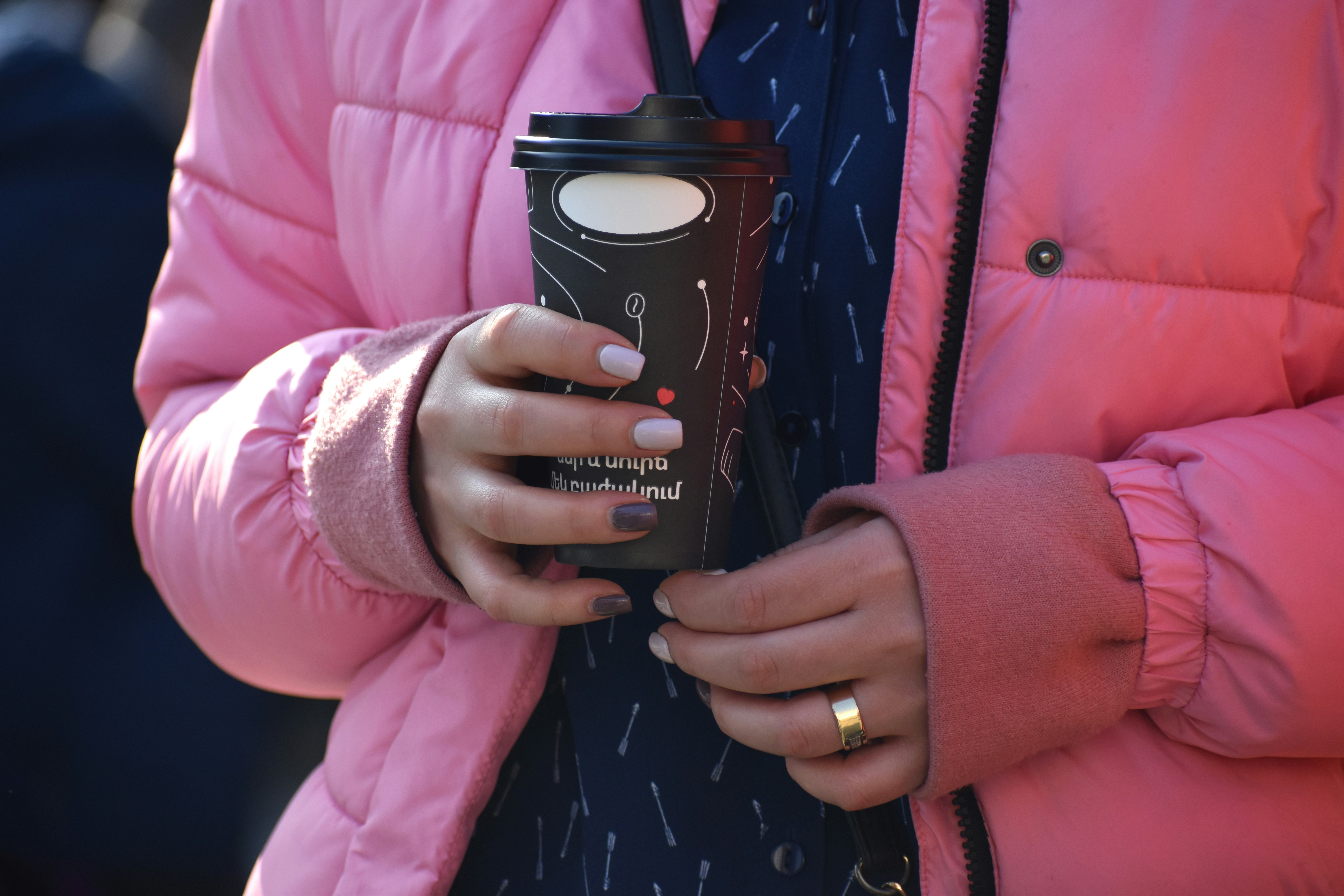 Close-up shot of a girl holding a coffee cup in the street.