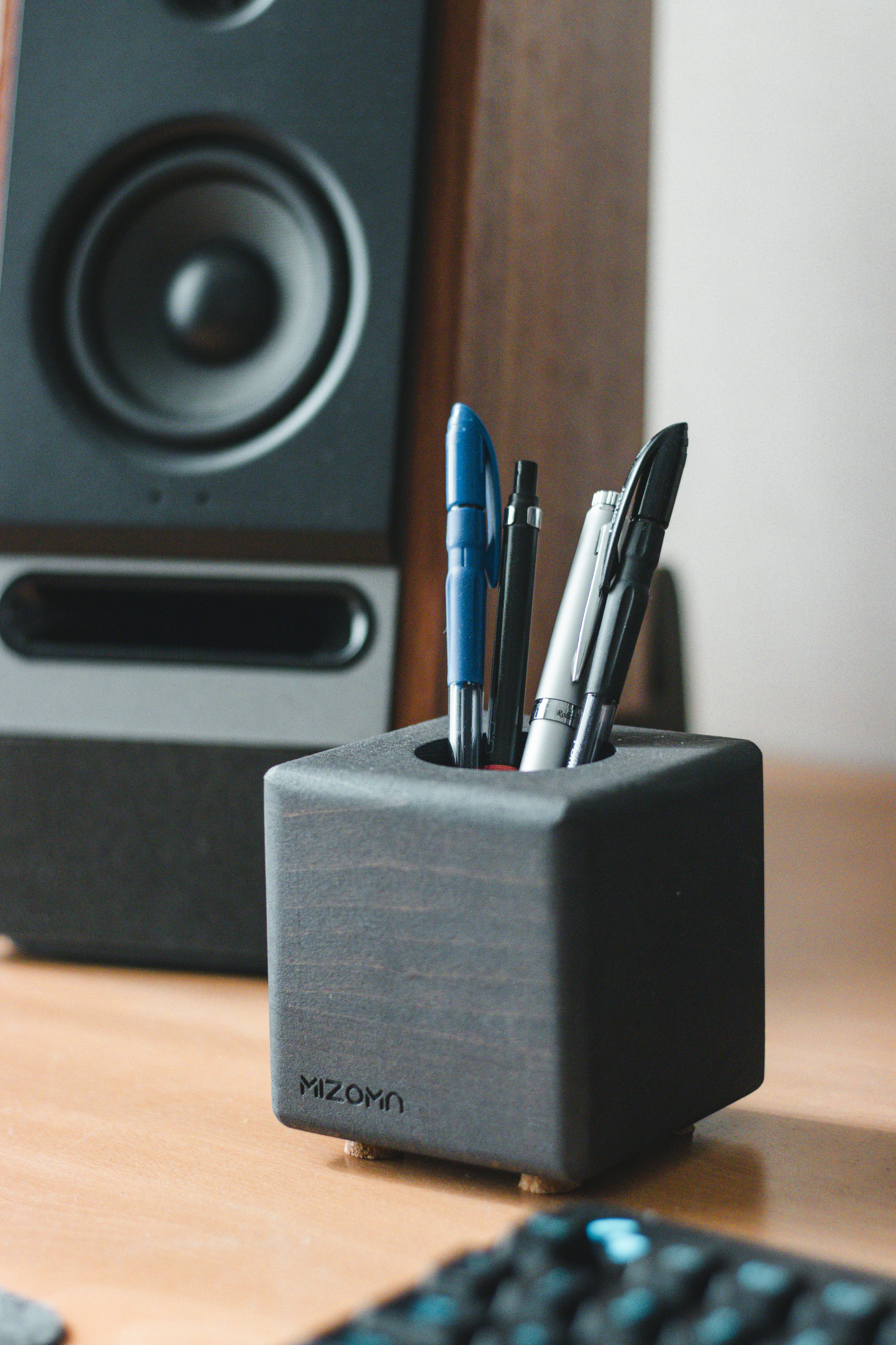 Stylish pen holder filled with various pens, positioned beside a sleek audio speaker on a wooden desk.