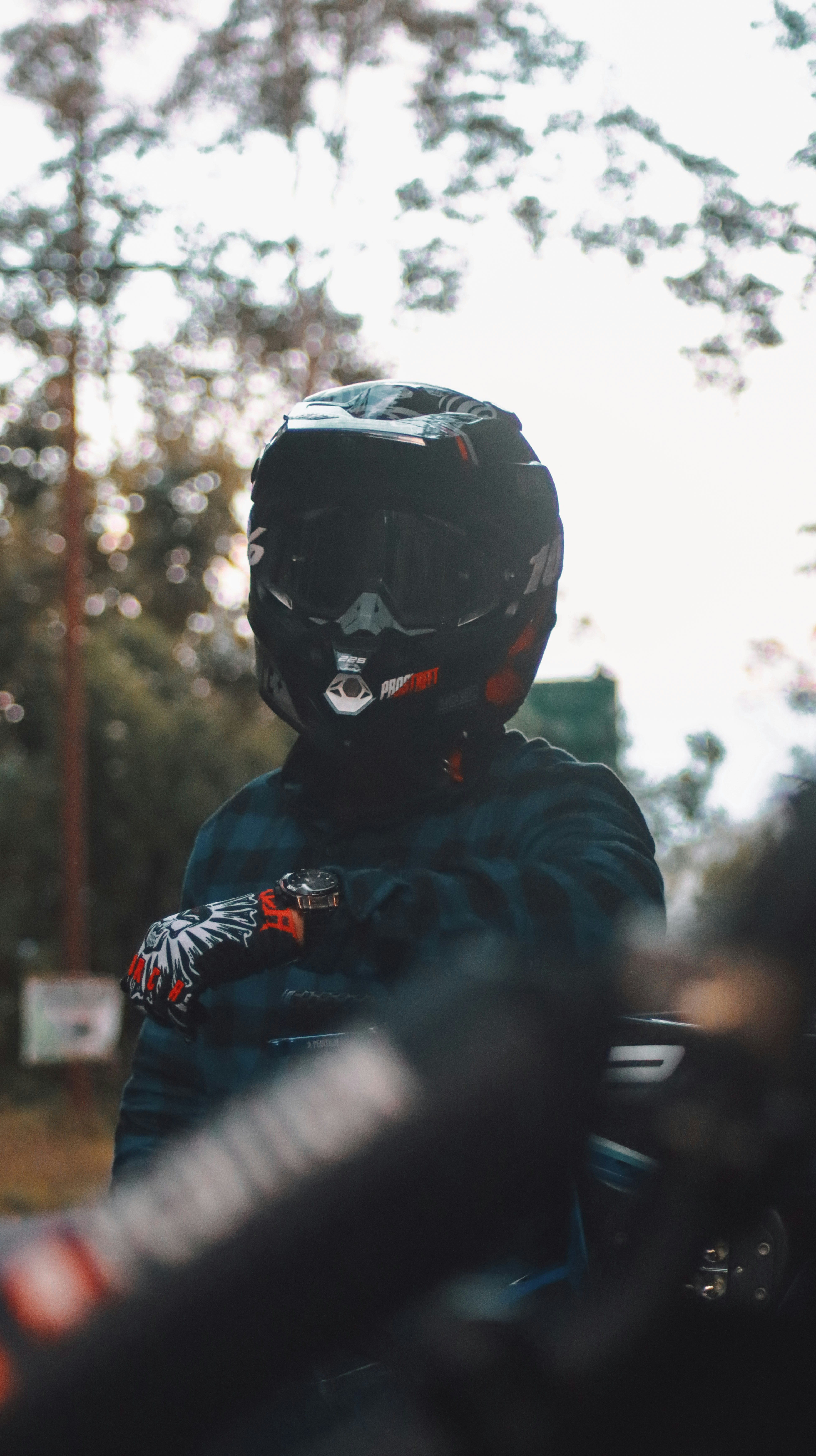 Motorcycle rider wearing a helmet and gloves, striking a pose amidst a blurred natural background. The scene conveys a sense of adventure and readiness.