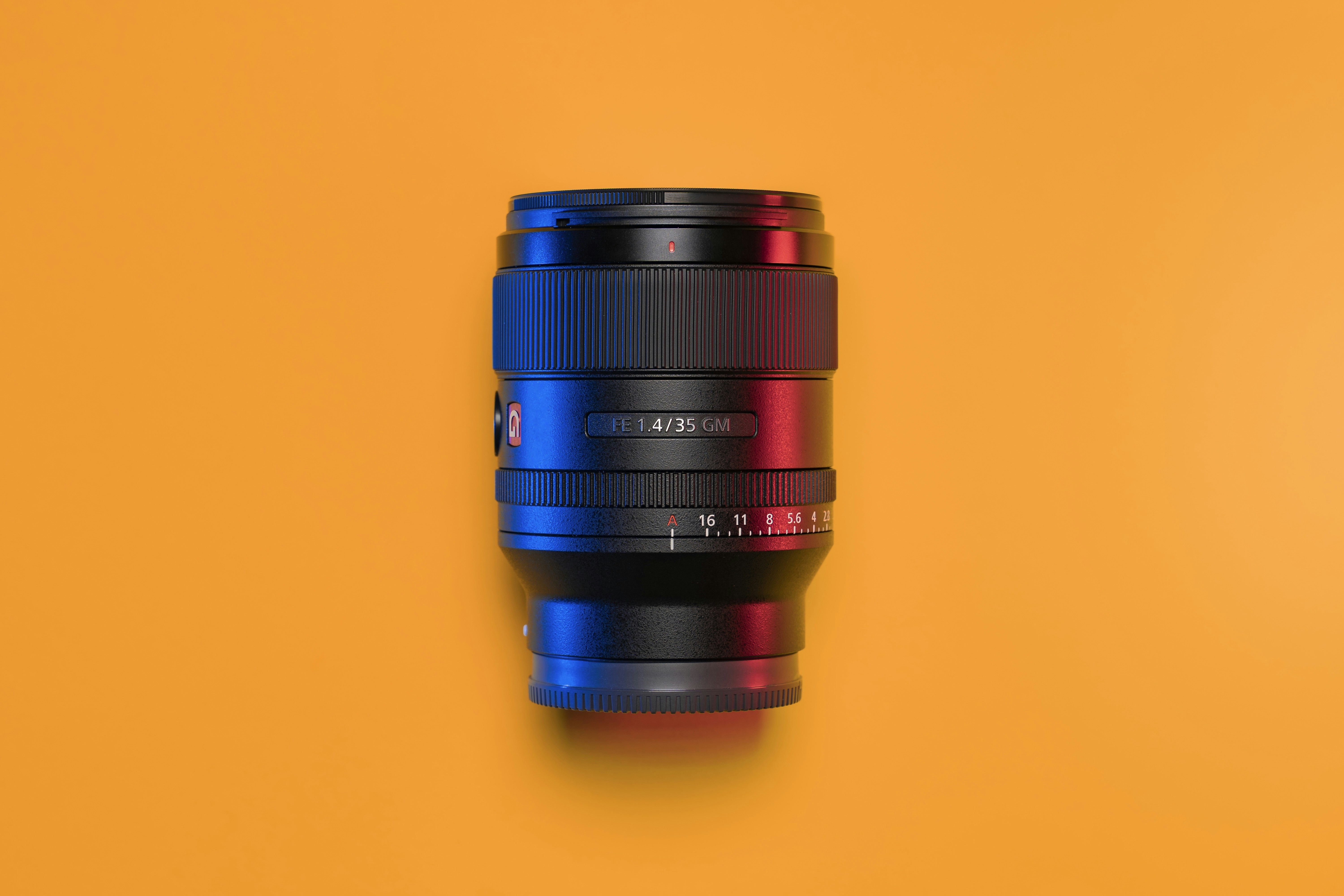 Close-up of a Sony lens against a vibrant orange background, showcasing its sleek design and intricate details.