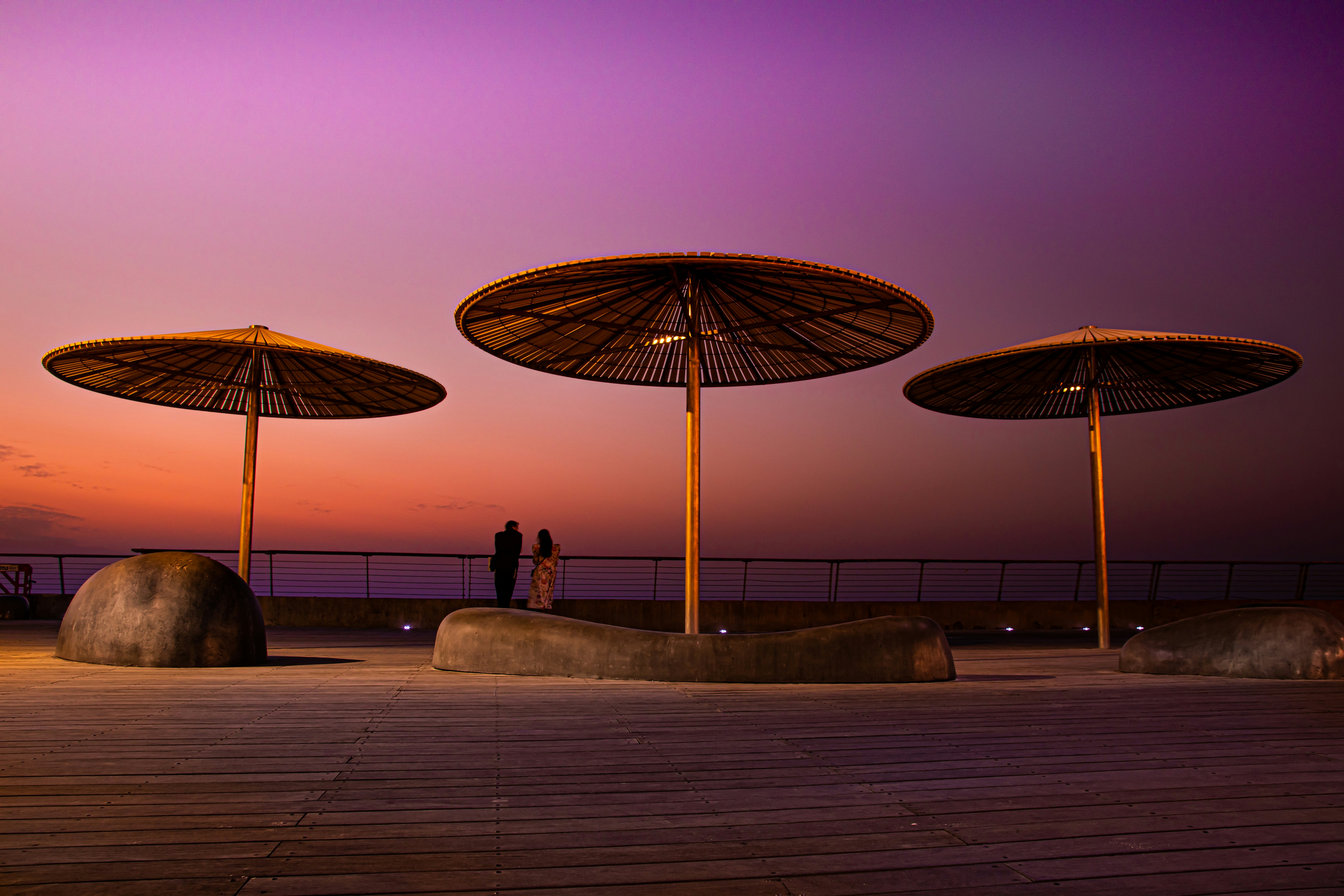 Silhouetted Couple Beneath Ocean-Blue Dusk with Umbrella Arches