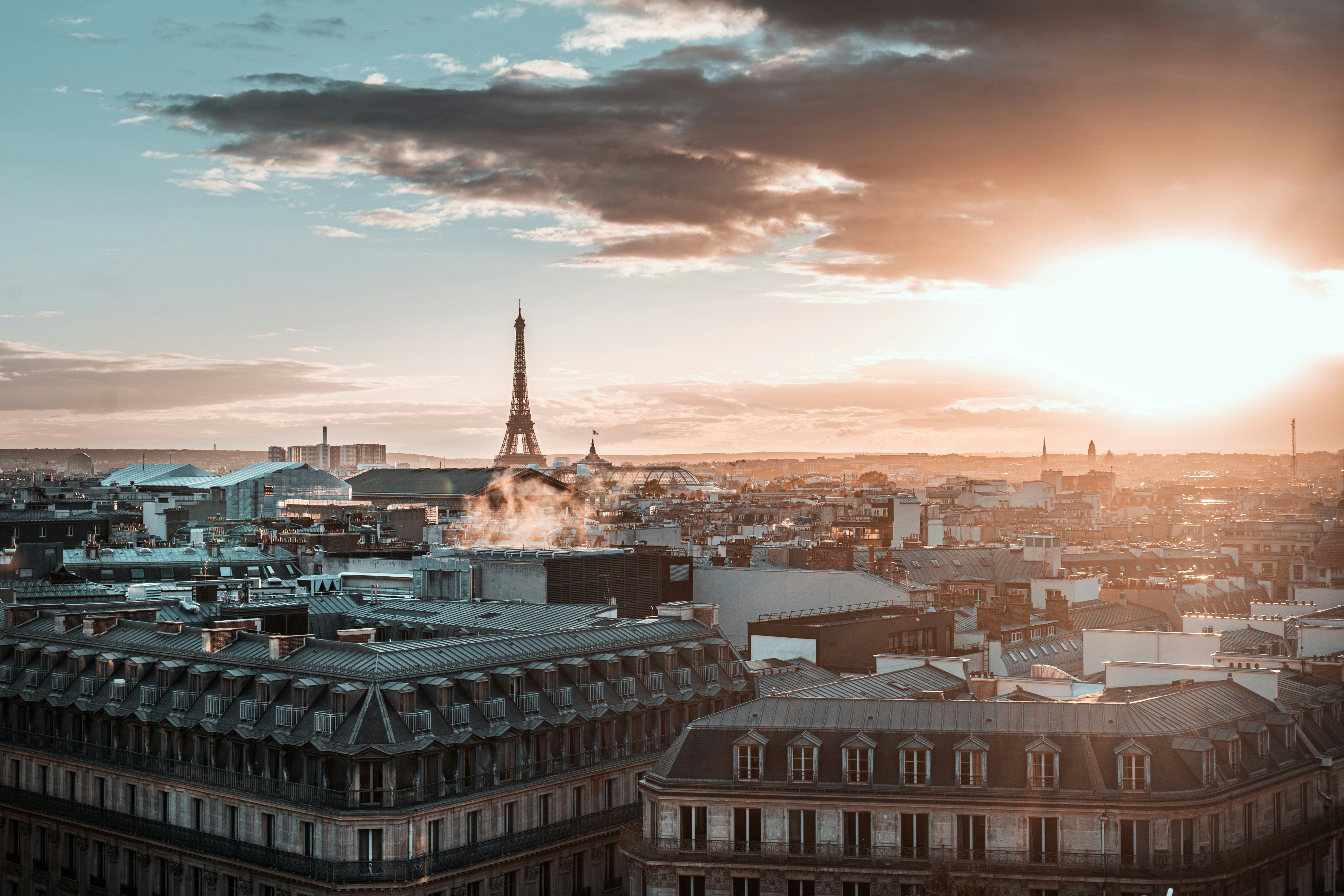 Eiffel Tower rising above Parisian rooftops as the sun sets, casting warm hues across the cityscape.