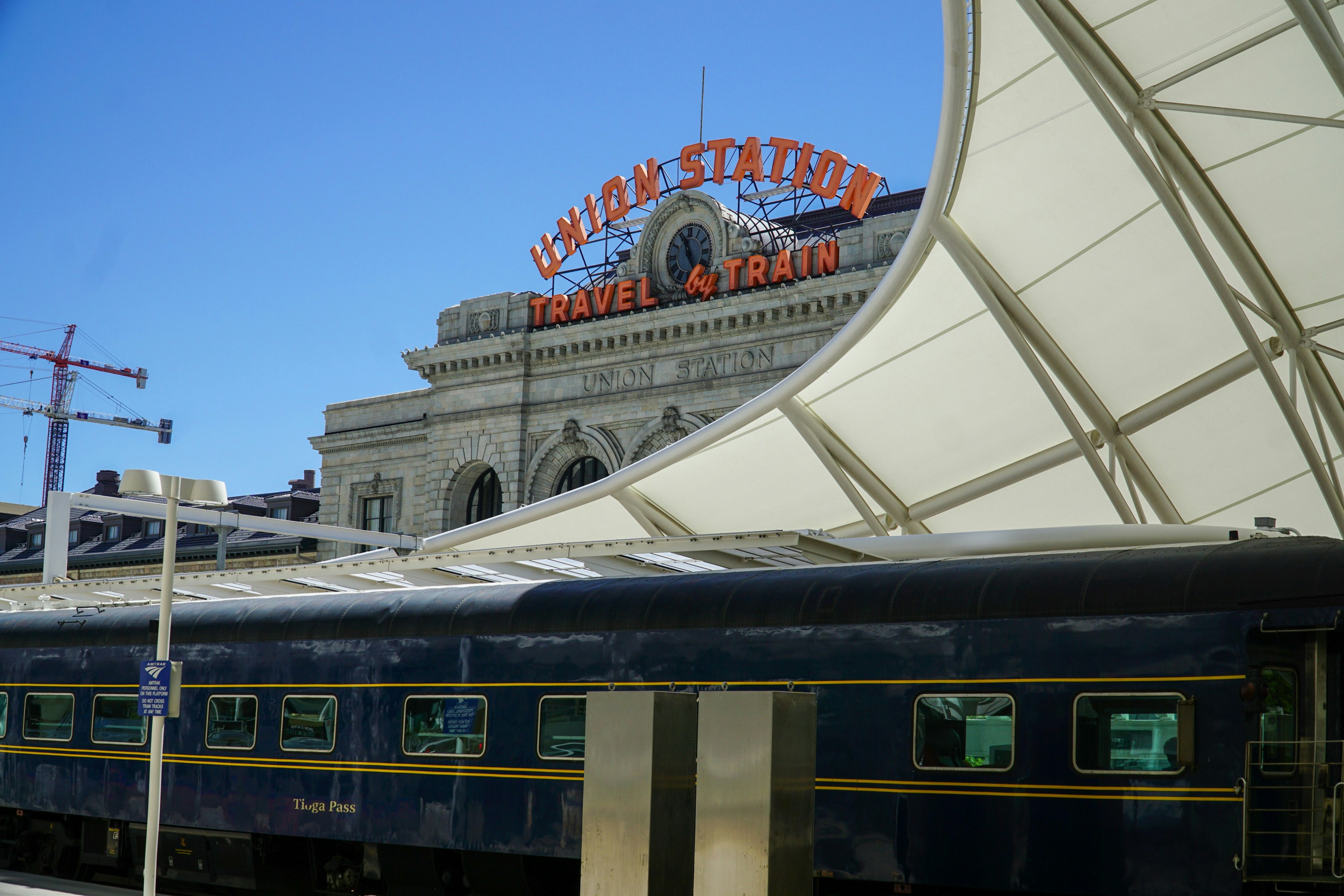Historic Union Station sign illuminated against a clear blue sky, with a vintage train parked beneath a contemporary canopy.