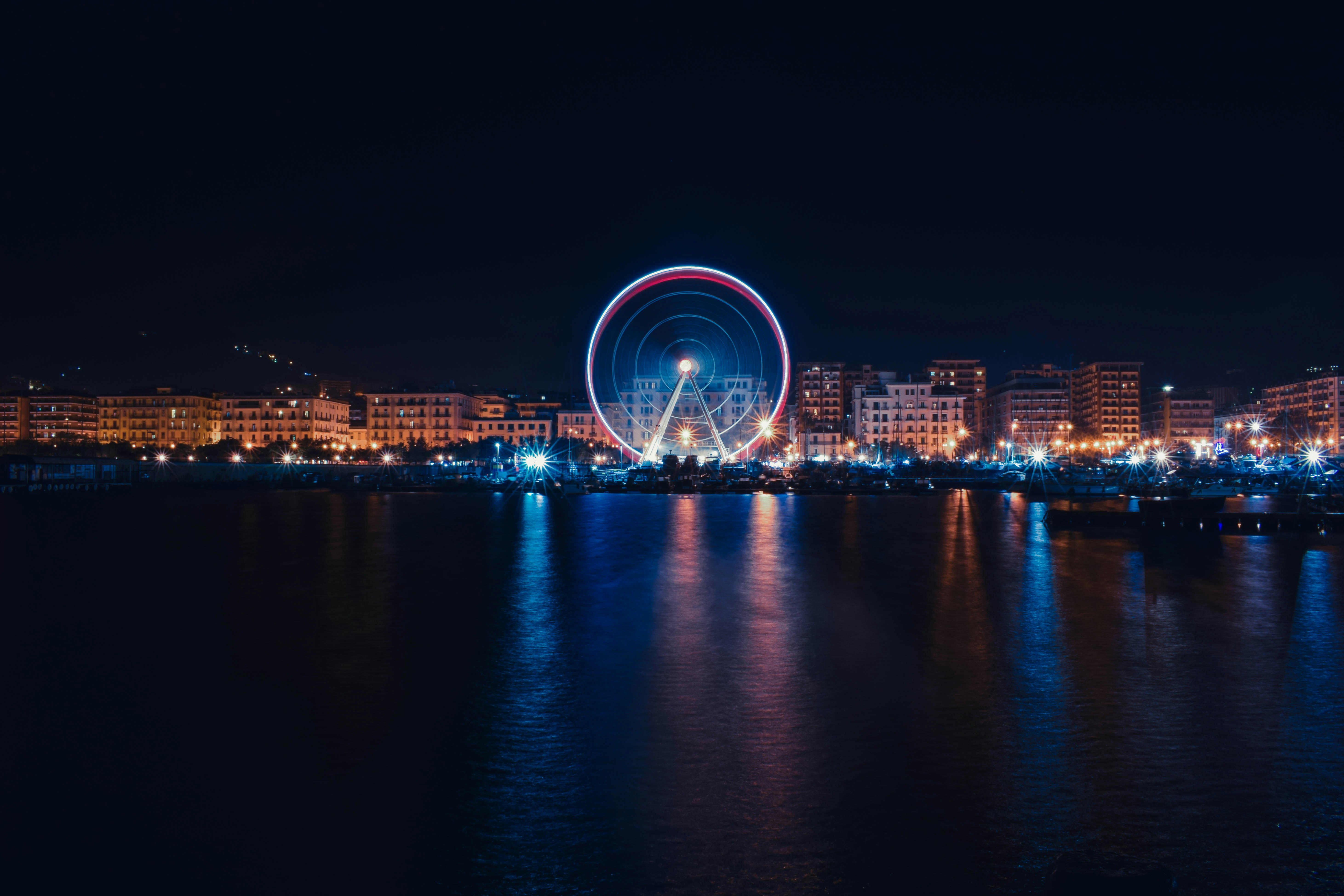 Illuminated Ferris wheel glowing against a vibrant cityscape reflected in calm waters at night.