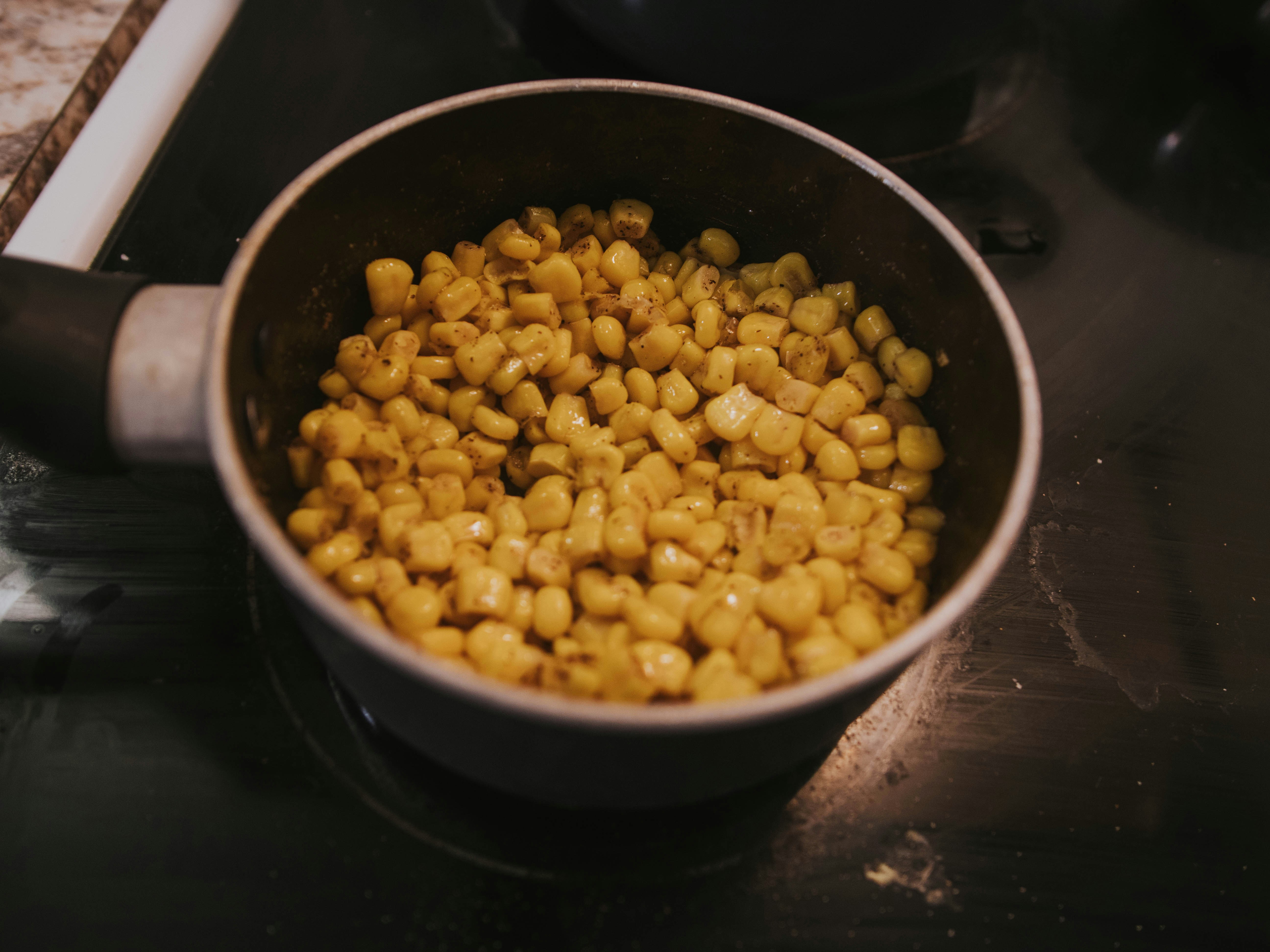 Cooked corn kernels simmering in a pot on a stovetop, showcasing a home-cooking scene.